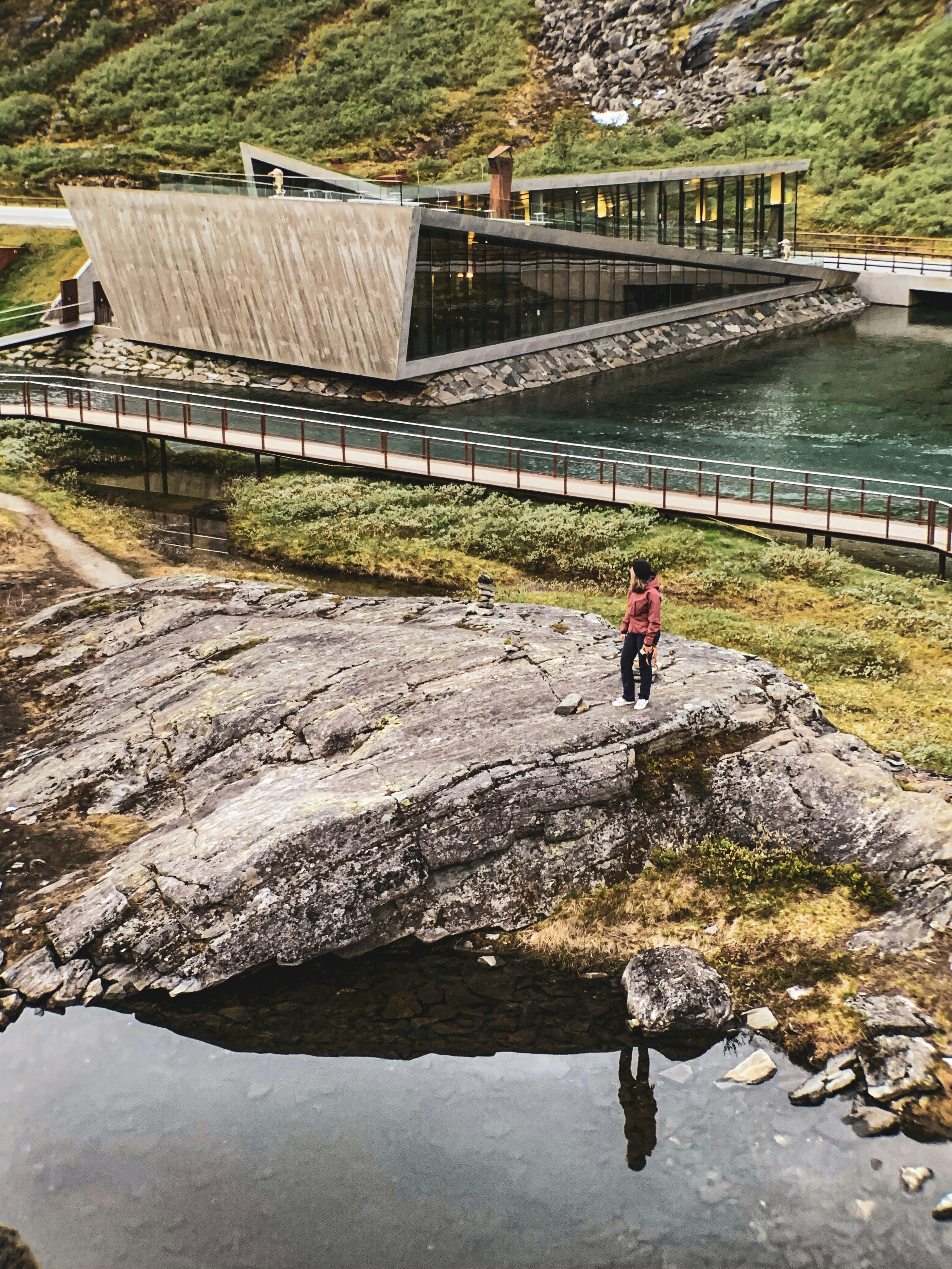 Lone Wanderer on Granite Edge with a Modern Waterside Pavilion