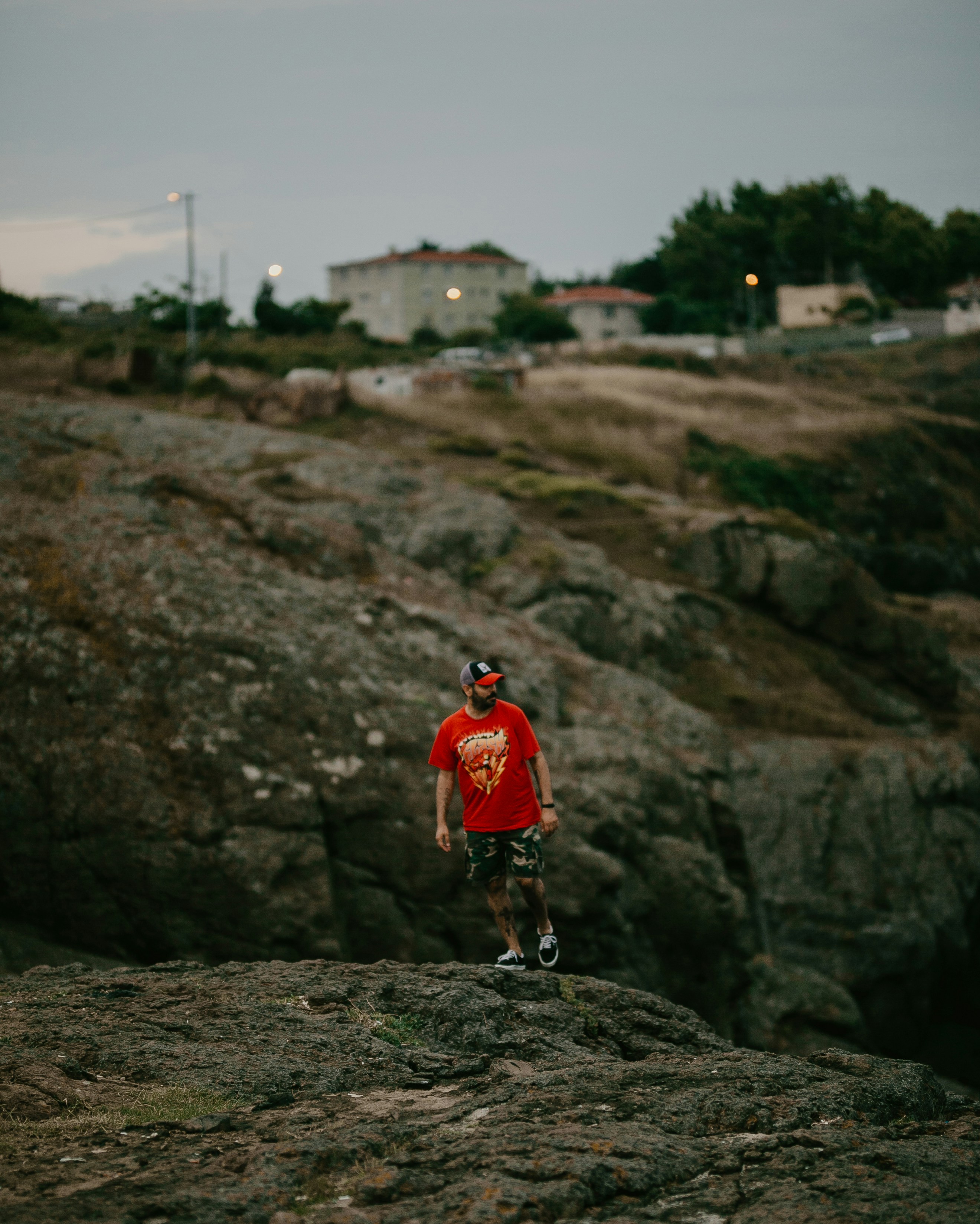 Lone Figure in a Red Tee Stands on Coastal Rocks at Dusk
