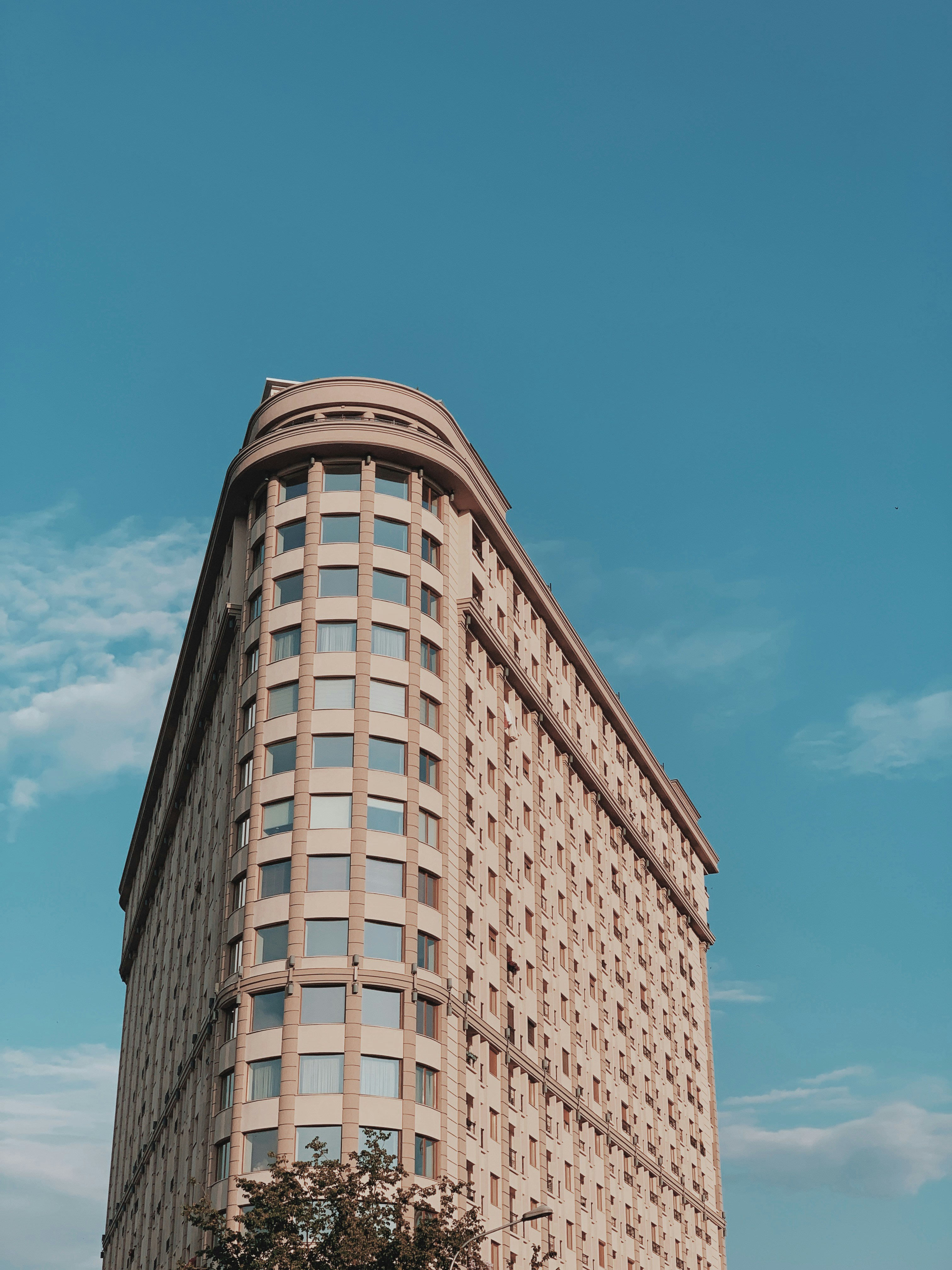 A towering building with a curved top and large windows, framed by a clear blue sky and scattered clouds.