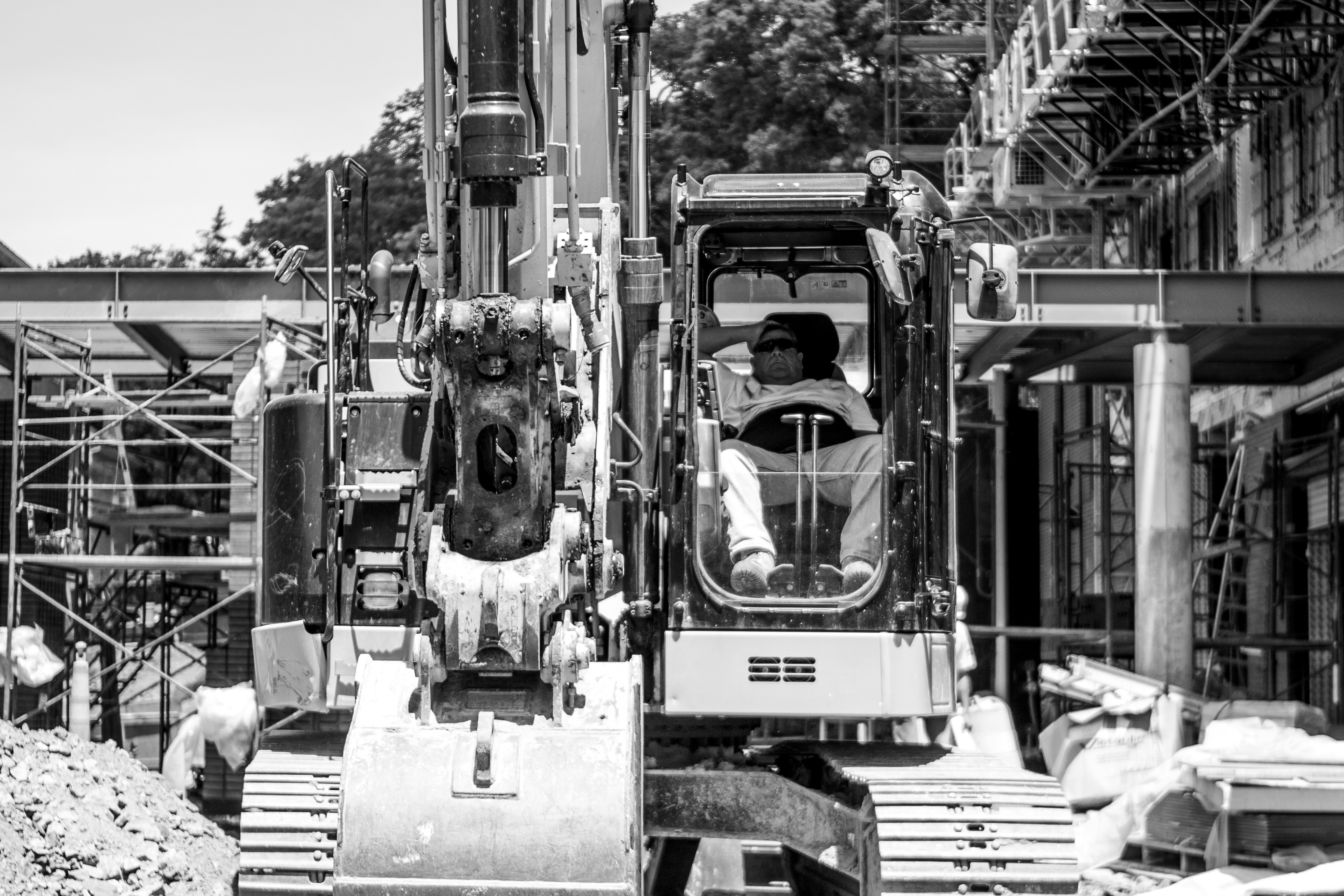 Excavator operator focused on the task at hand amidst a construction site filled with scaffolding and materials.