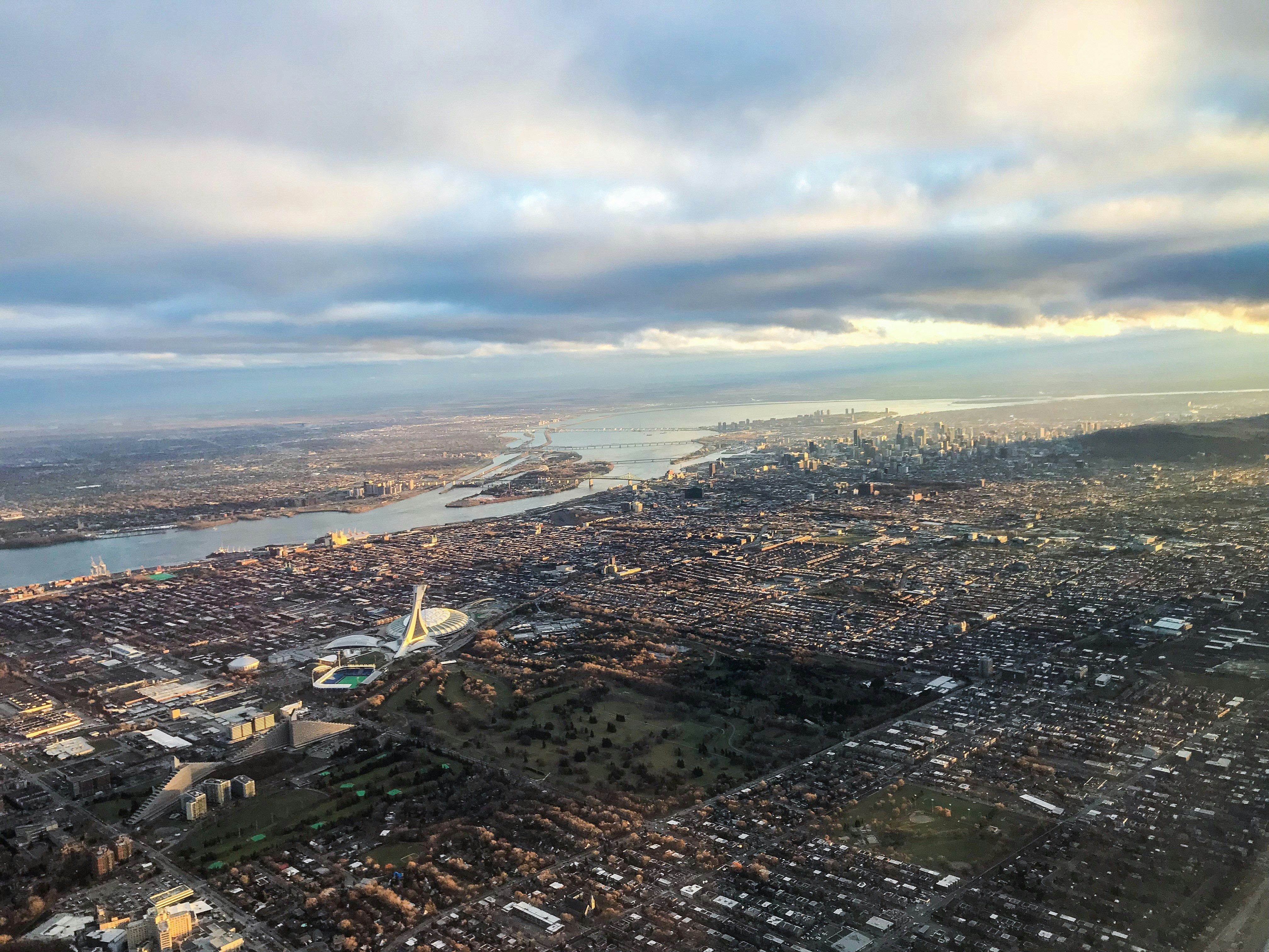 Aerial view of a sprawling cityscape meeting the sea under a sky with streaks of clouds and soft sunset hues.