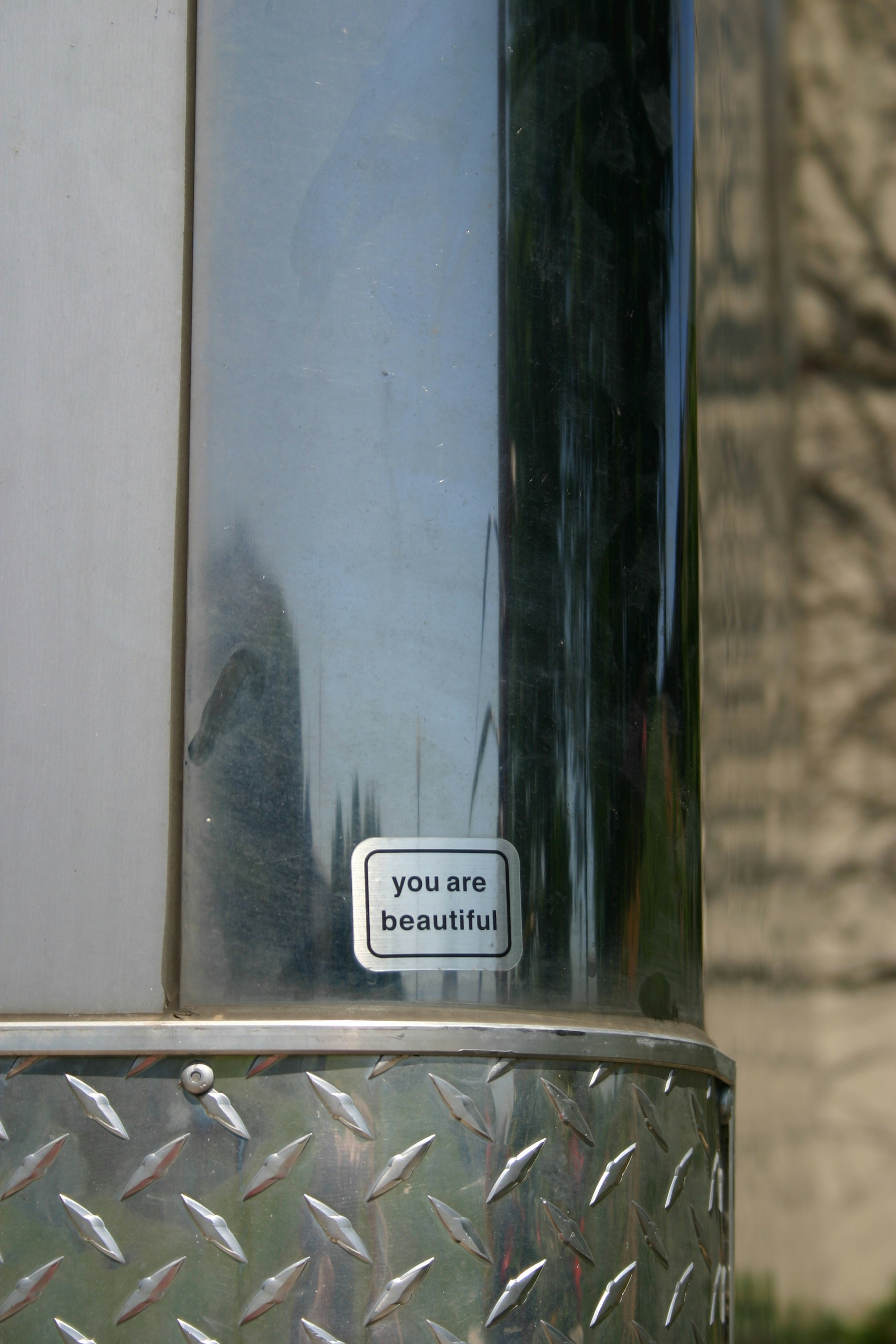 A reflective surface showcases a small metallic sticker with the words 'you are beautiful' affixed to it. The contrasting textures highlight the message's significance.