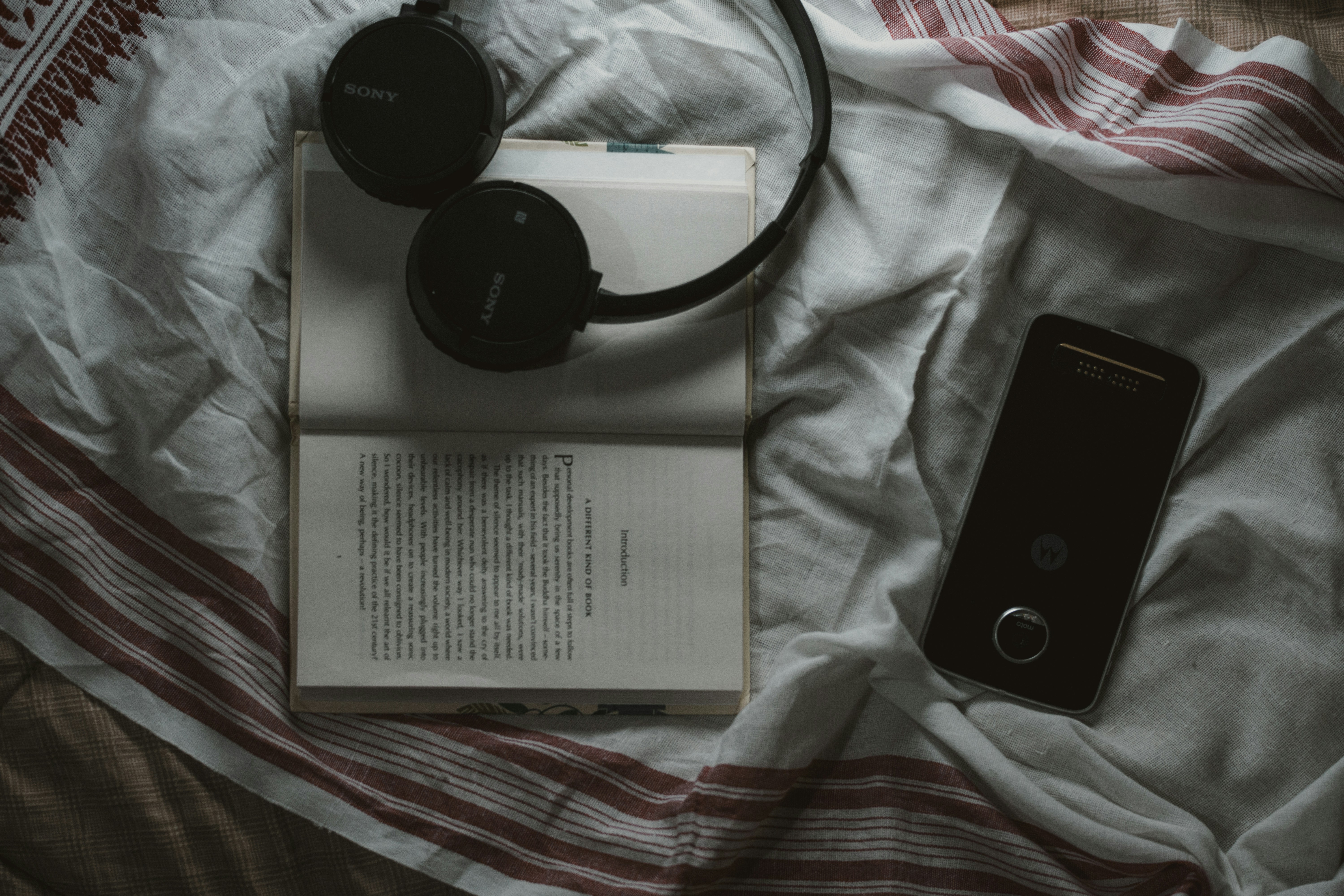 Open book resting on a textured surface, accompanied by headphones and a smartphone, creating a serene atmosphere for relaxation.