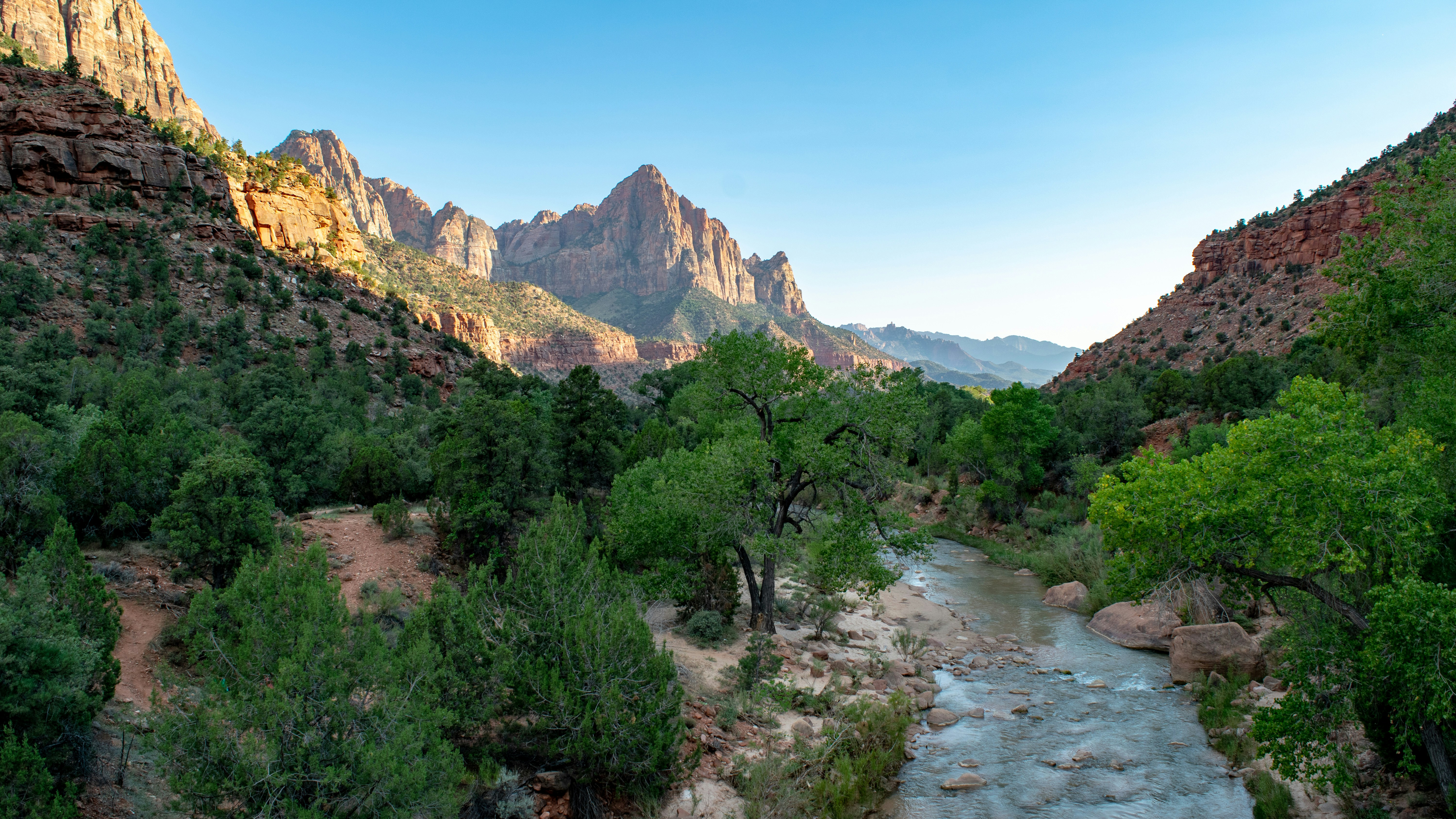 River winding through lush green trees and rugged canyon cliffs under a clear blue sky.