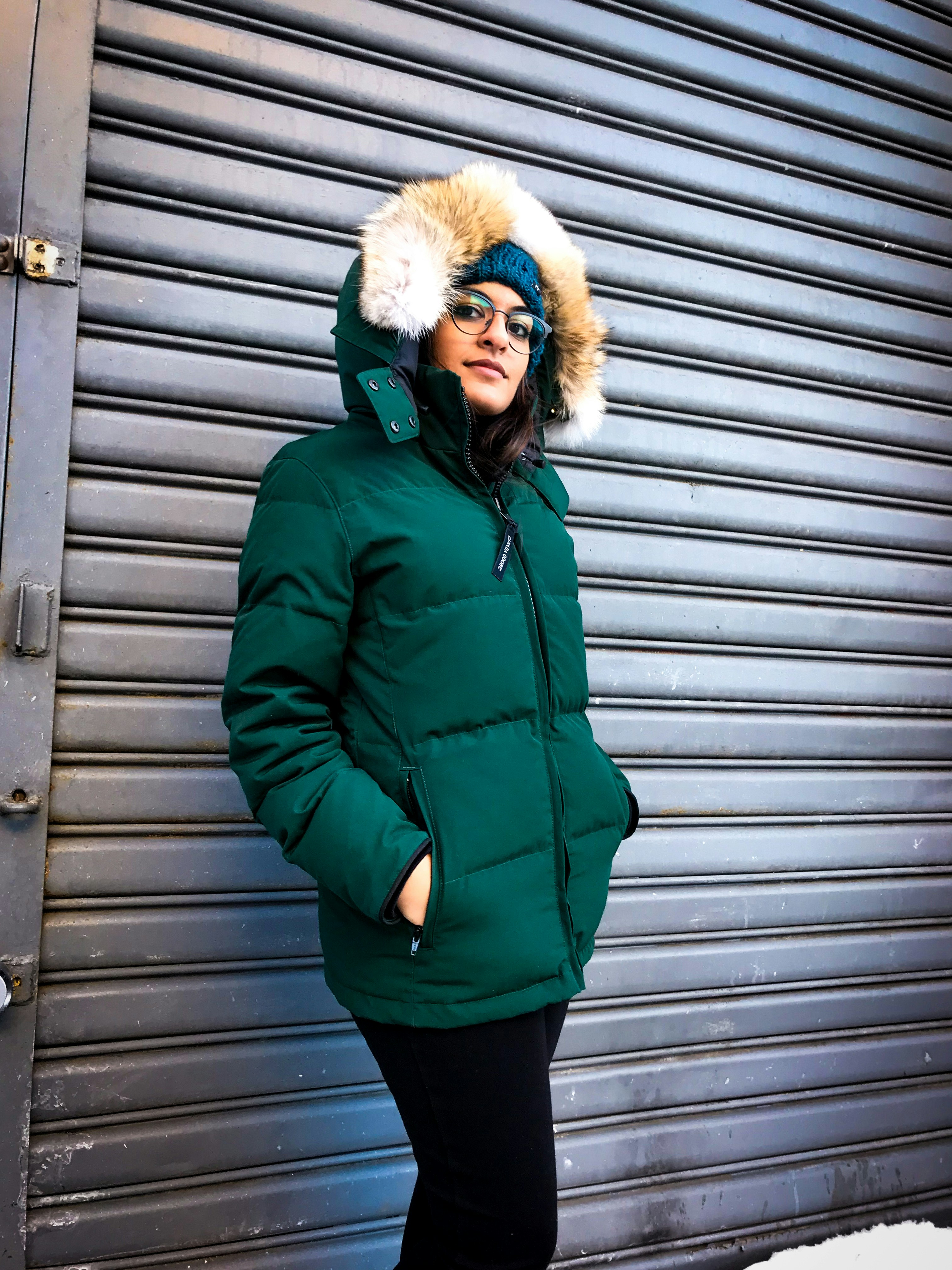 A young woman in a green puffer jacket poses confidently against a textured gray backdrop, showcasing winter fashion with a cozy flair.