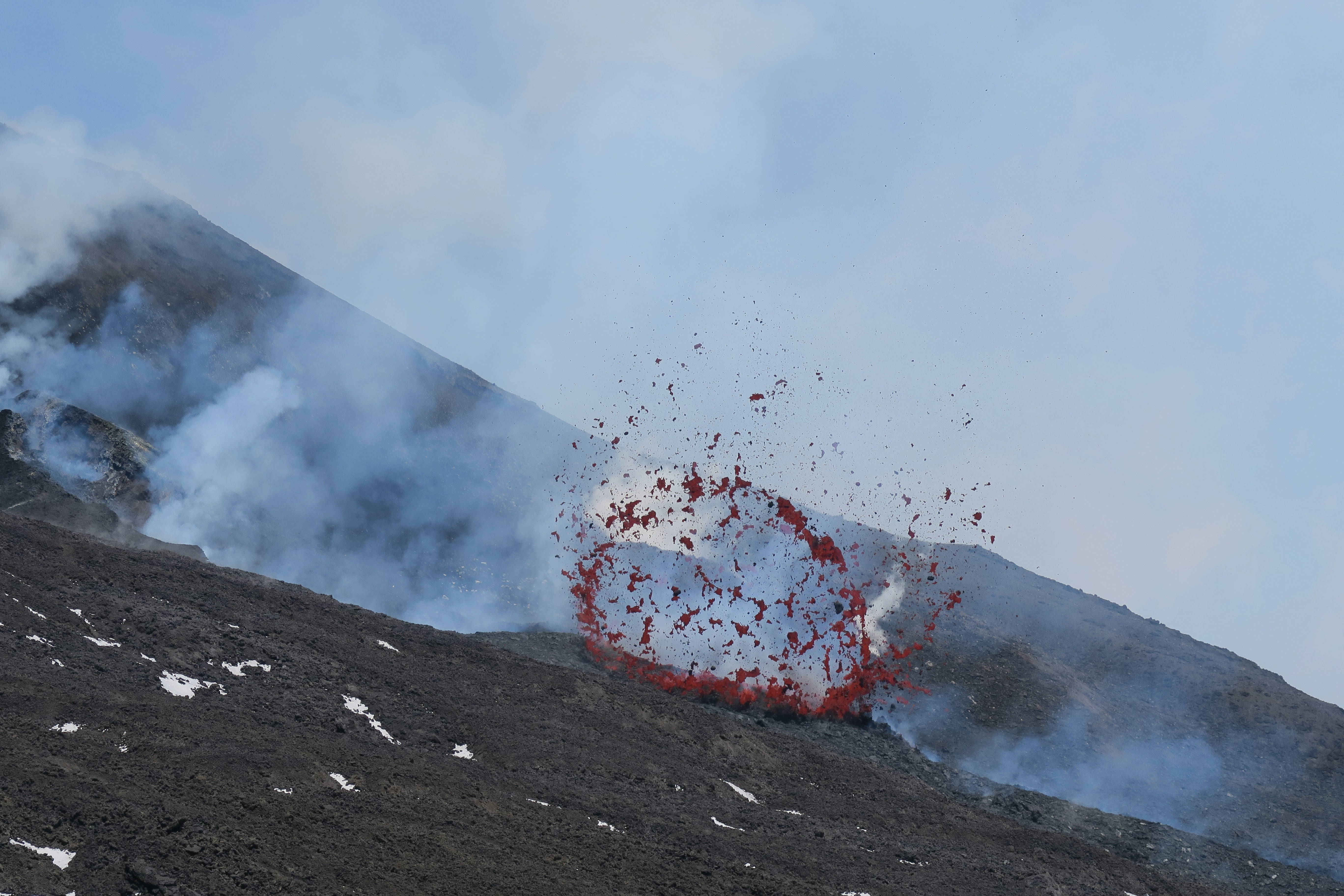 Molten lava bursts from a volcanic vent, creating a dramatic display against a smoky backdrop. The eruption captures the raw power of nature in motion.