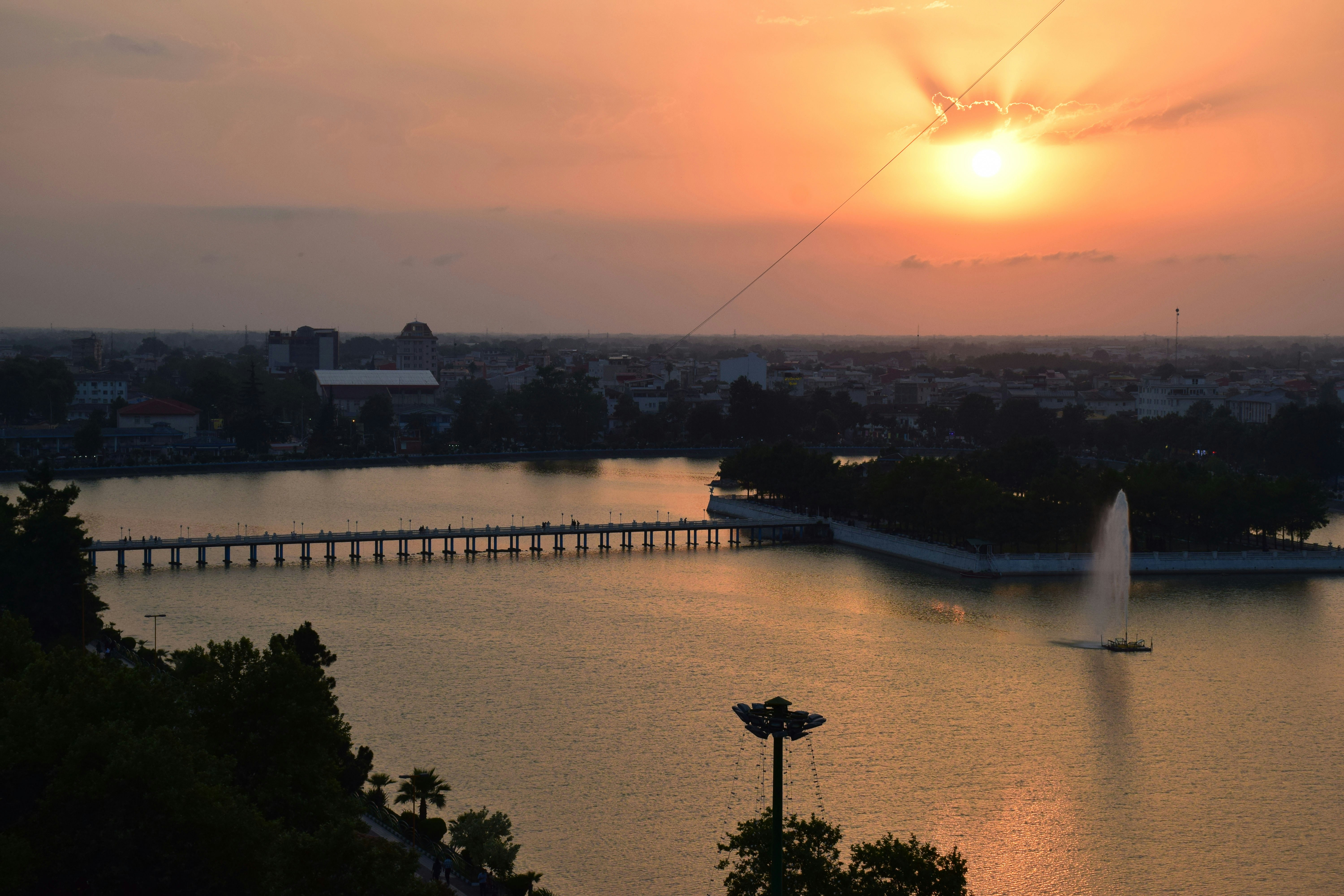 Sunset over a Quiet Lake: The Bridge's Arc and a Dancing Fountain
