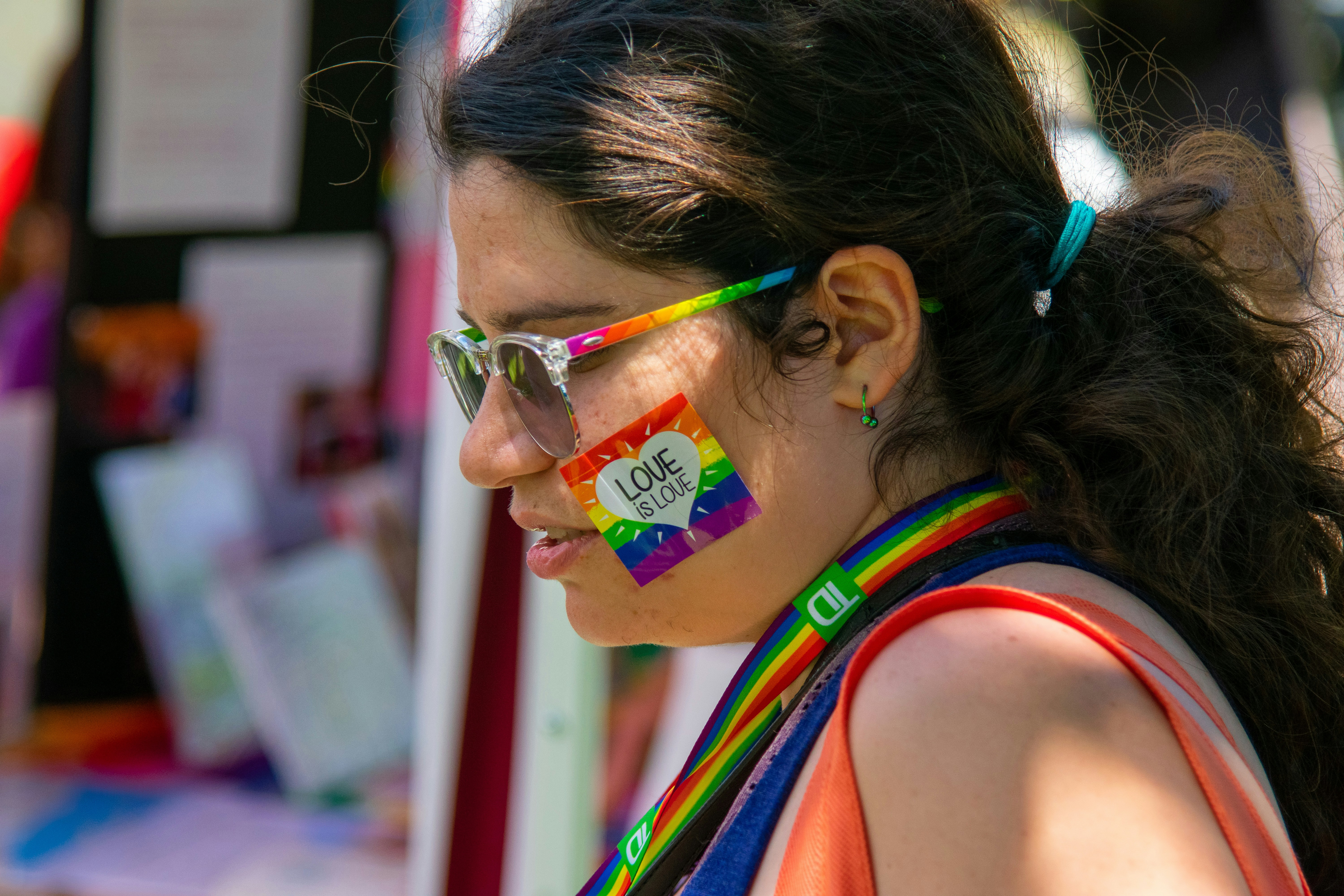 Person with colorful face paint and rainbow lanyard at outdoor event.