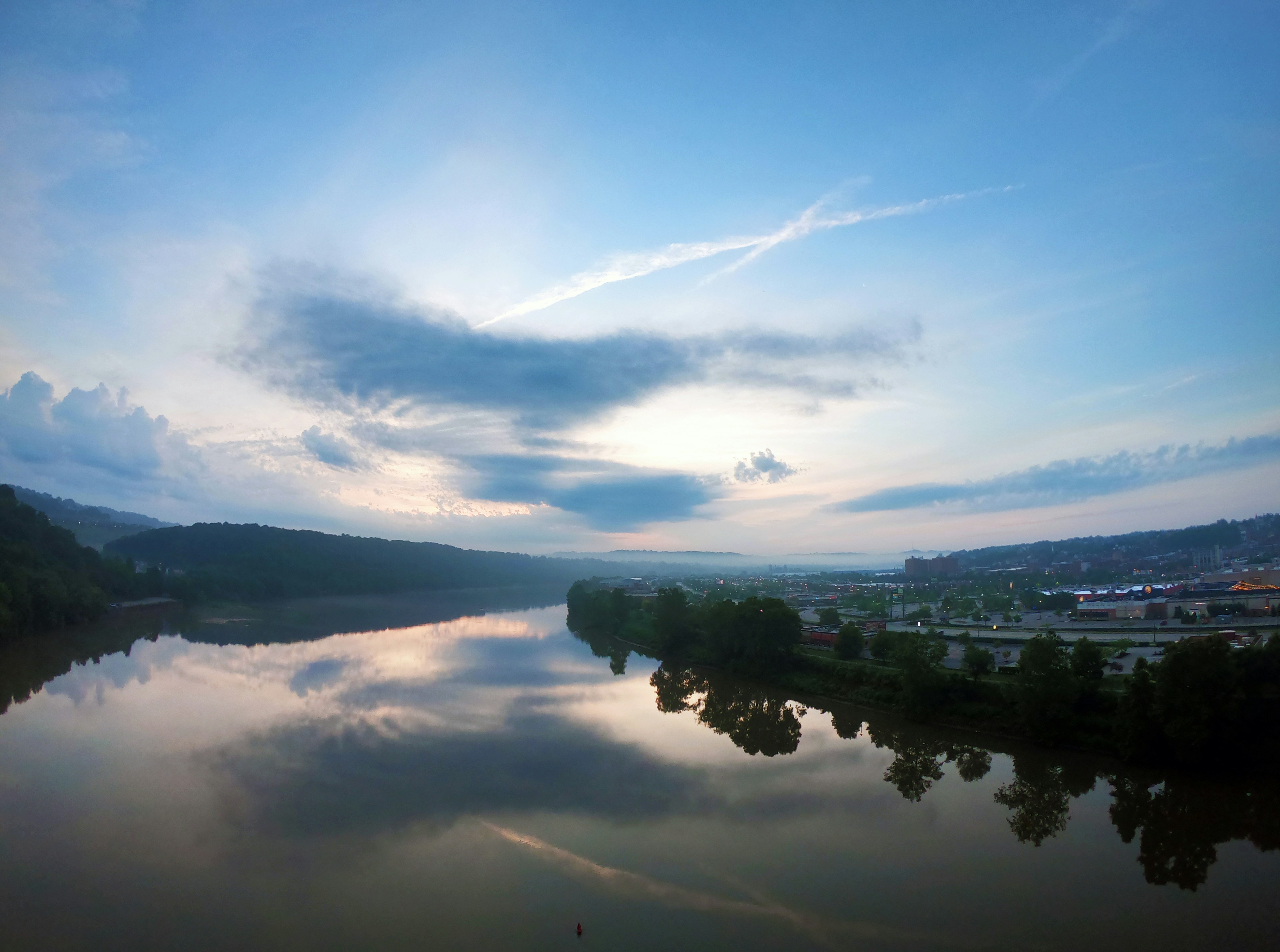 Clouds and trees mirrored on a calm river at dusk.