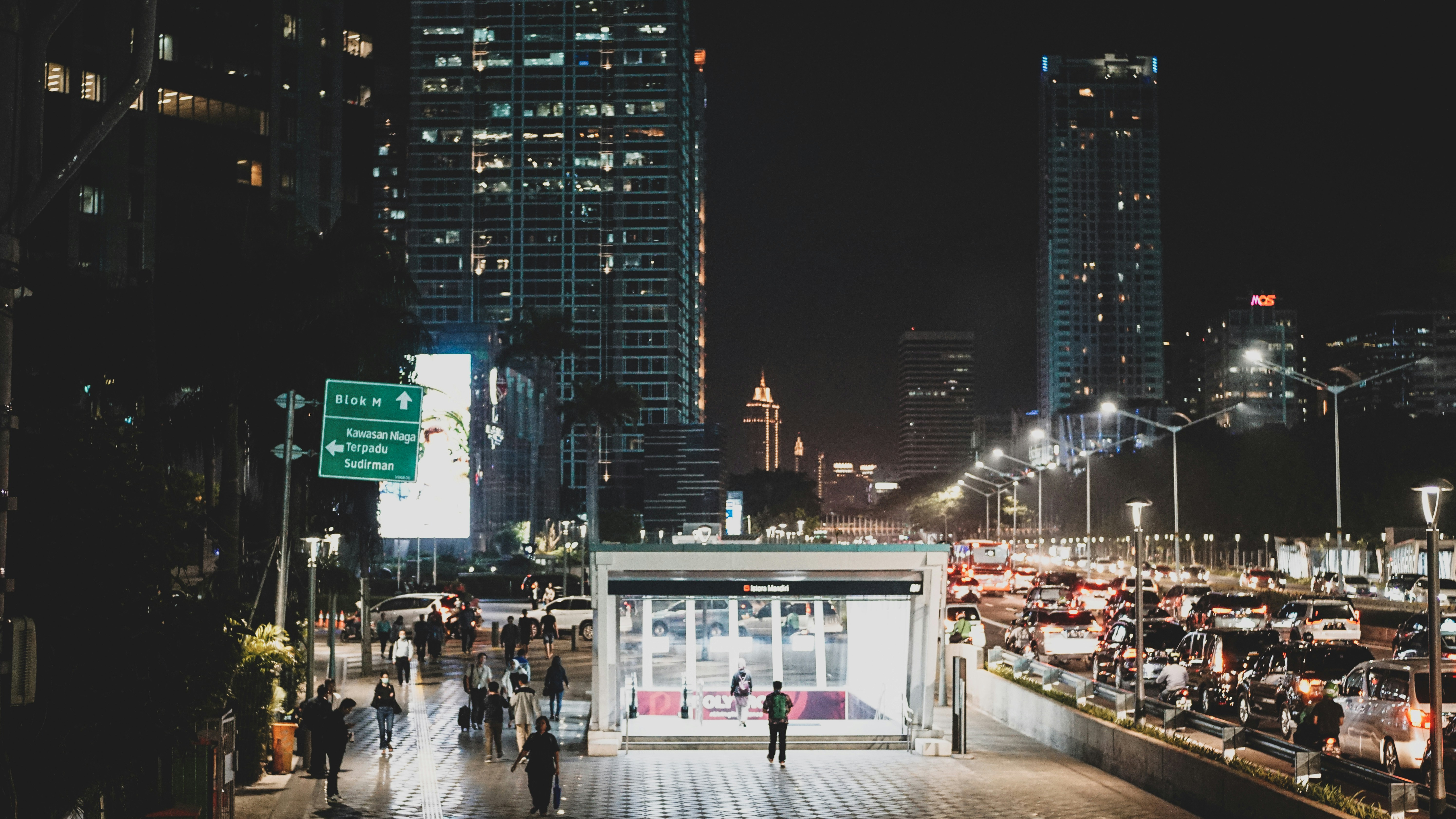 Bustling Jakarta street at night with pedestrians and traffic under city lights.