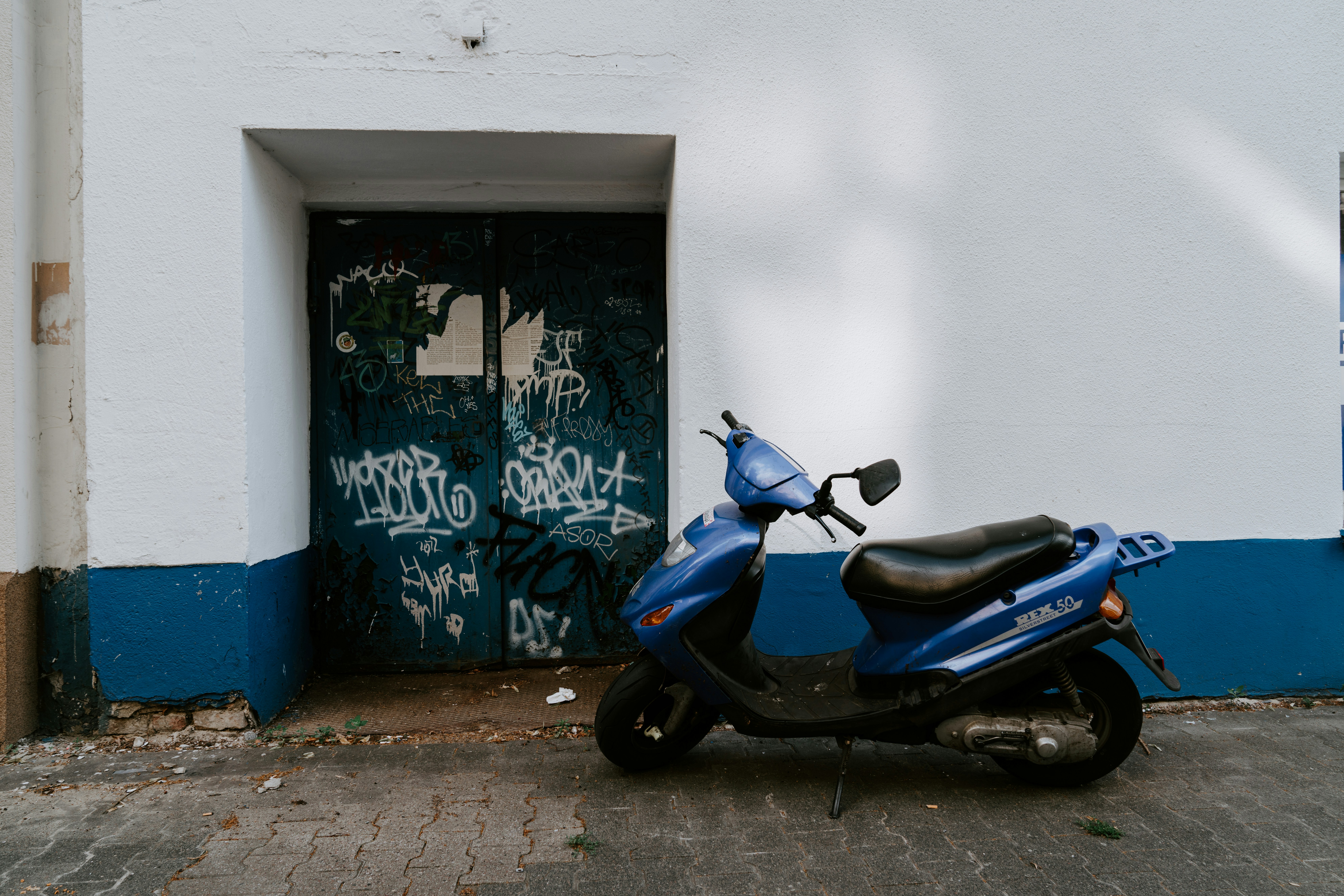Blue Scooter Quietly Poised Before a Graffiti-Splashed Garage Door