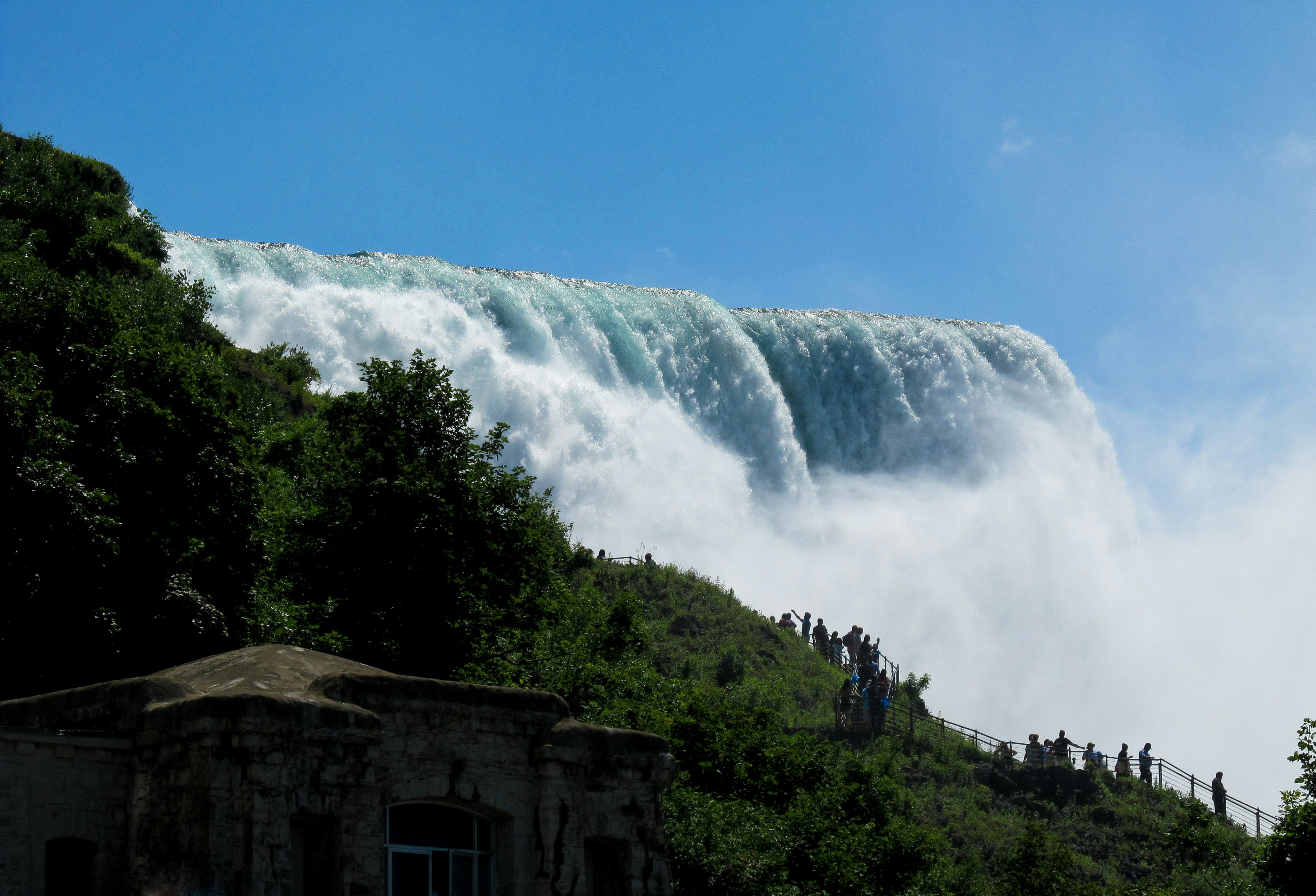 Large waterfall cascading over a lush, green cliff under a bright blue sky.
