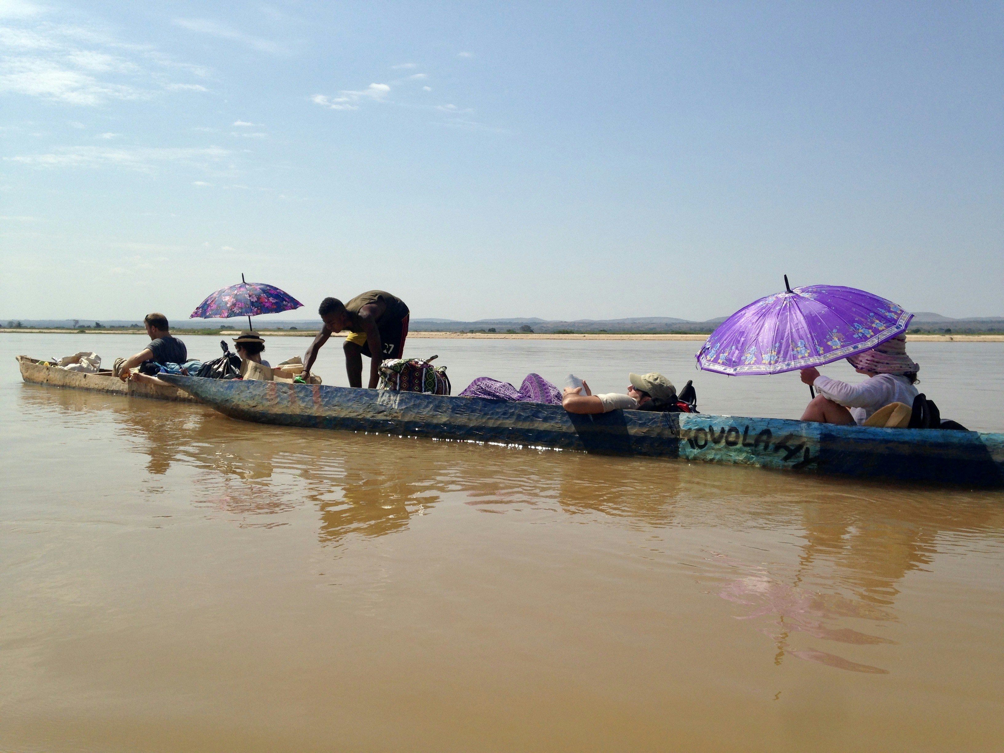 Canoe with purple umbrellas gliding along the Tsiribihina River under a clear sky.