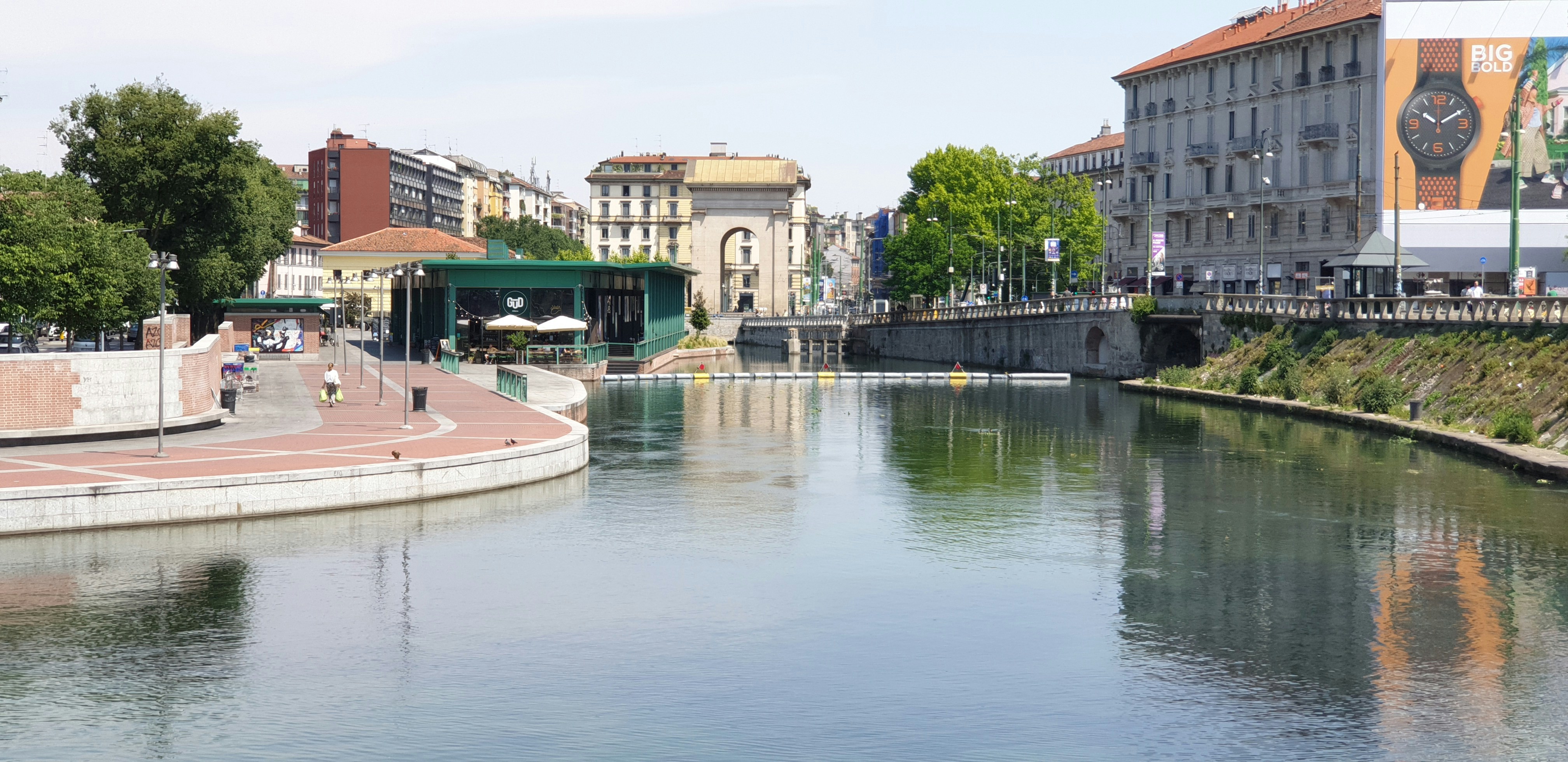 Tranquil canal flanked by historic buildings and lush greenery under a clear sky.