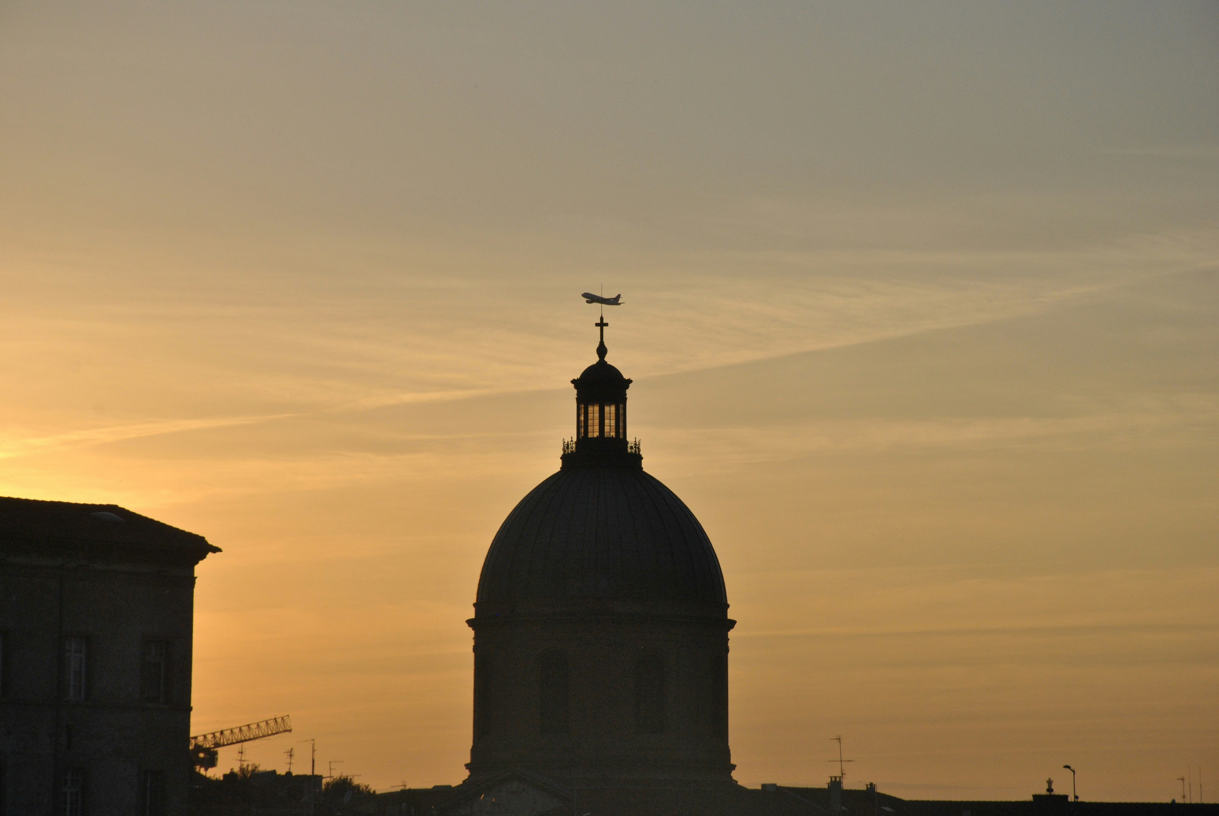 Silhouette of a domed building with a weathervane against a sunrise sky.