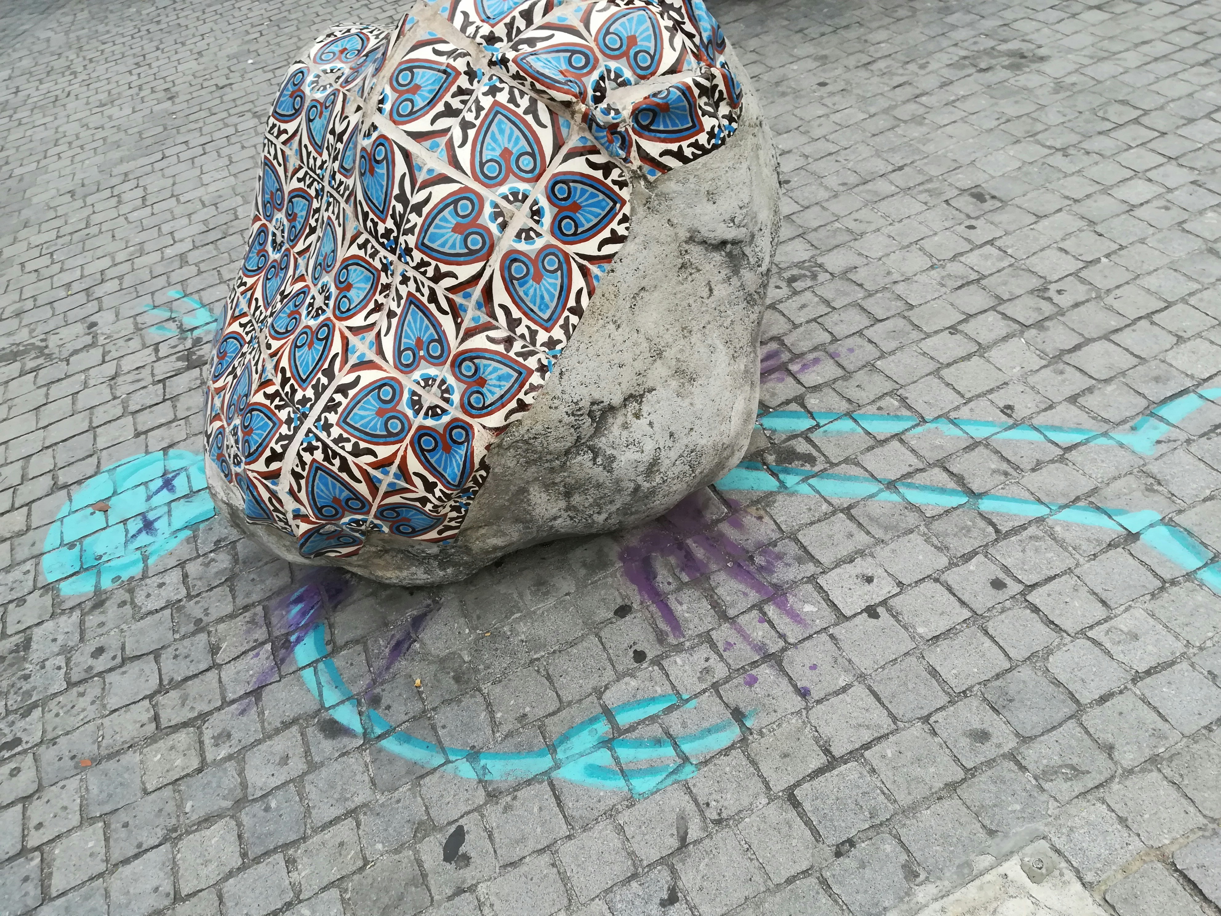 Decoratively painted rock blending with vibrant street art on cobblestone pavement.
