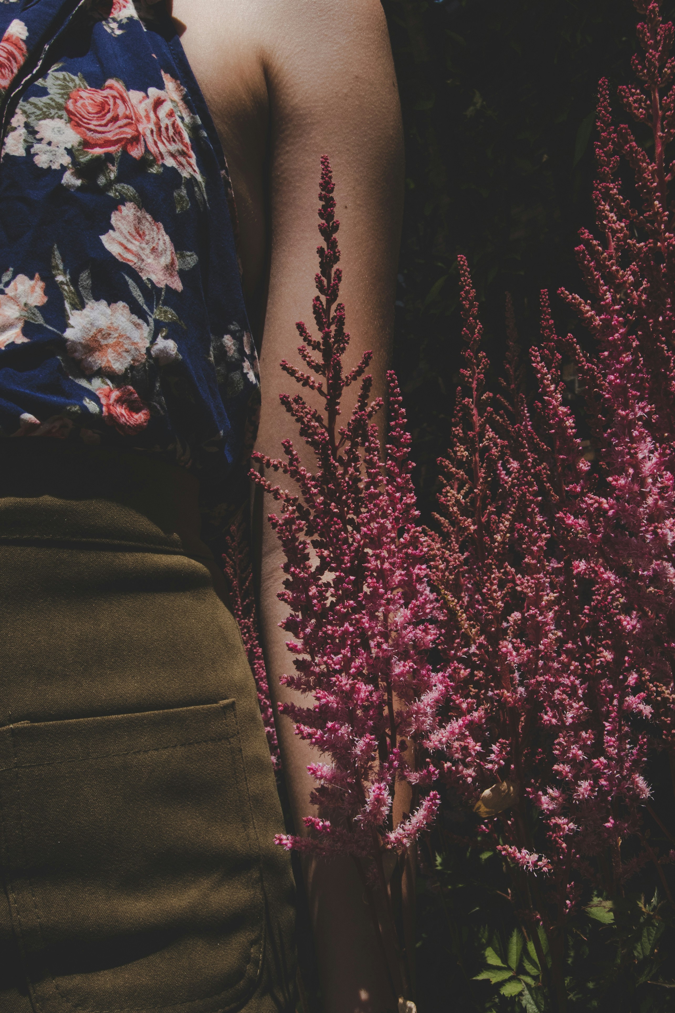 A close-up of a person’s arm adorned with vibrant pink flowers, showcasing a floral-patterned top against a lush backdrop.