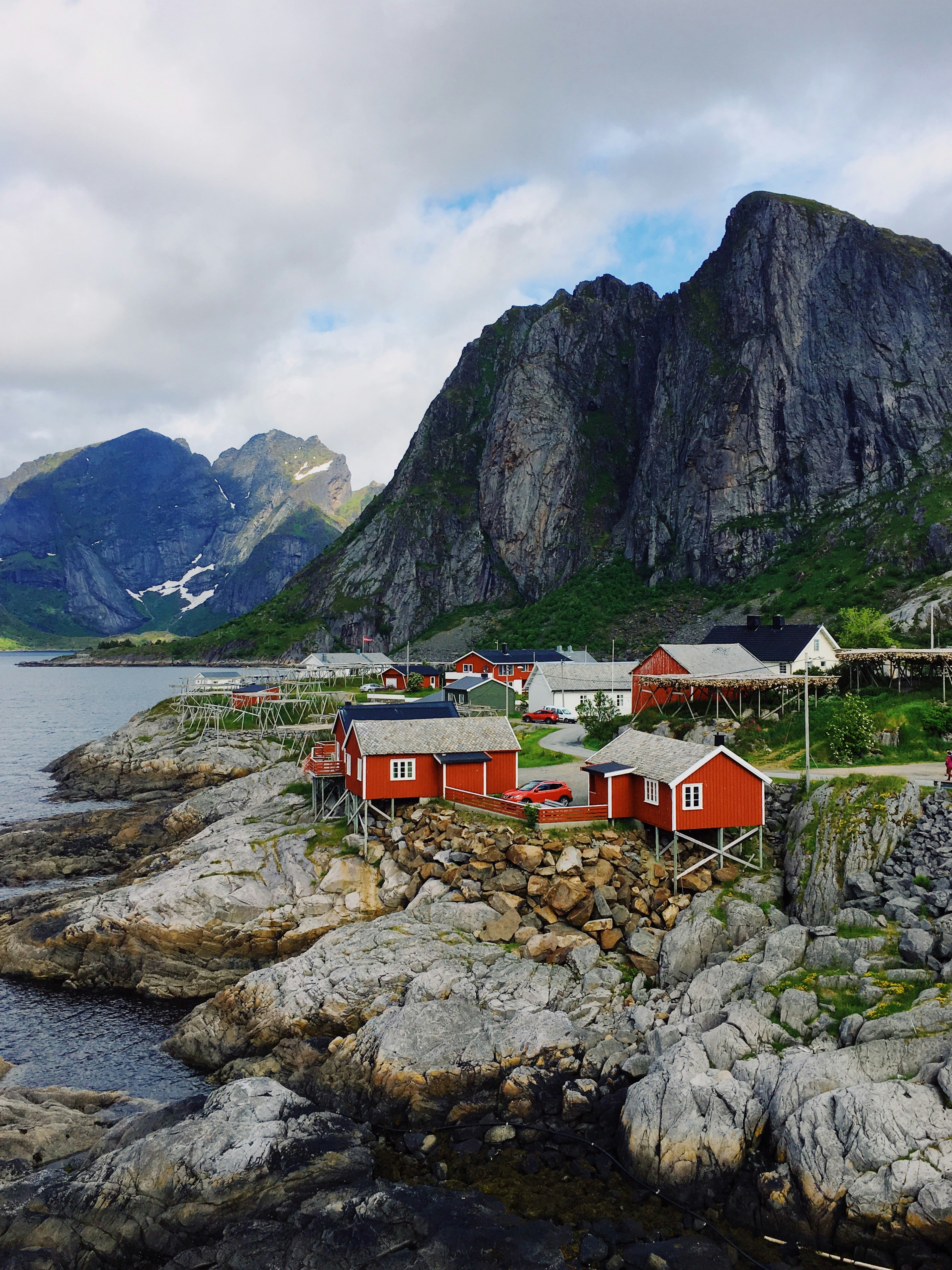 Charming red cabins perched on rocky shores, framed by towering mountains and a serene fjord. A tranquil scene of coastal living.