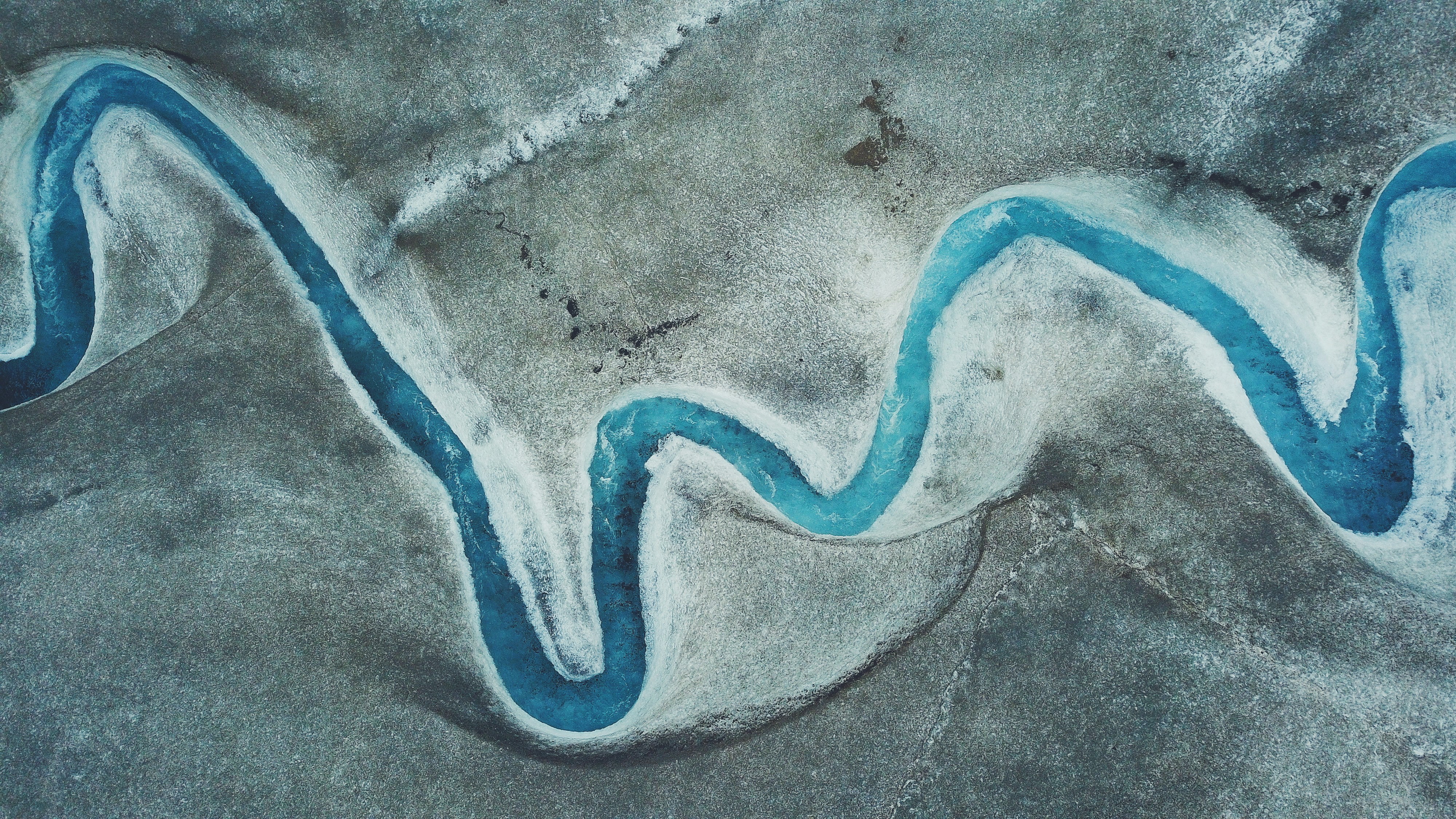 Winding river carving through a textured landscape, showcasing vibrant blue water against a muted backdrop. 