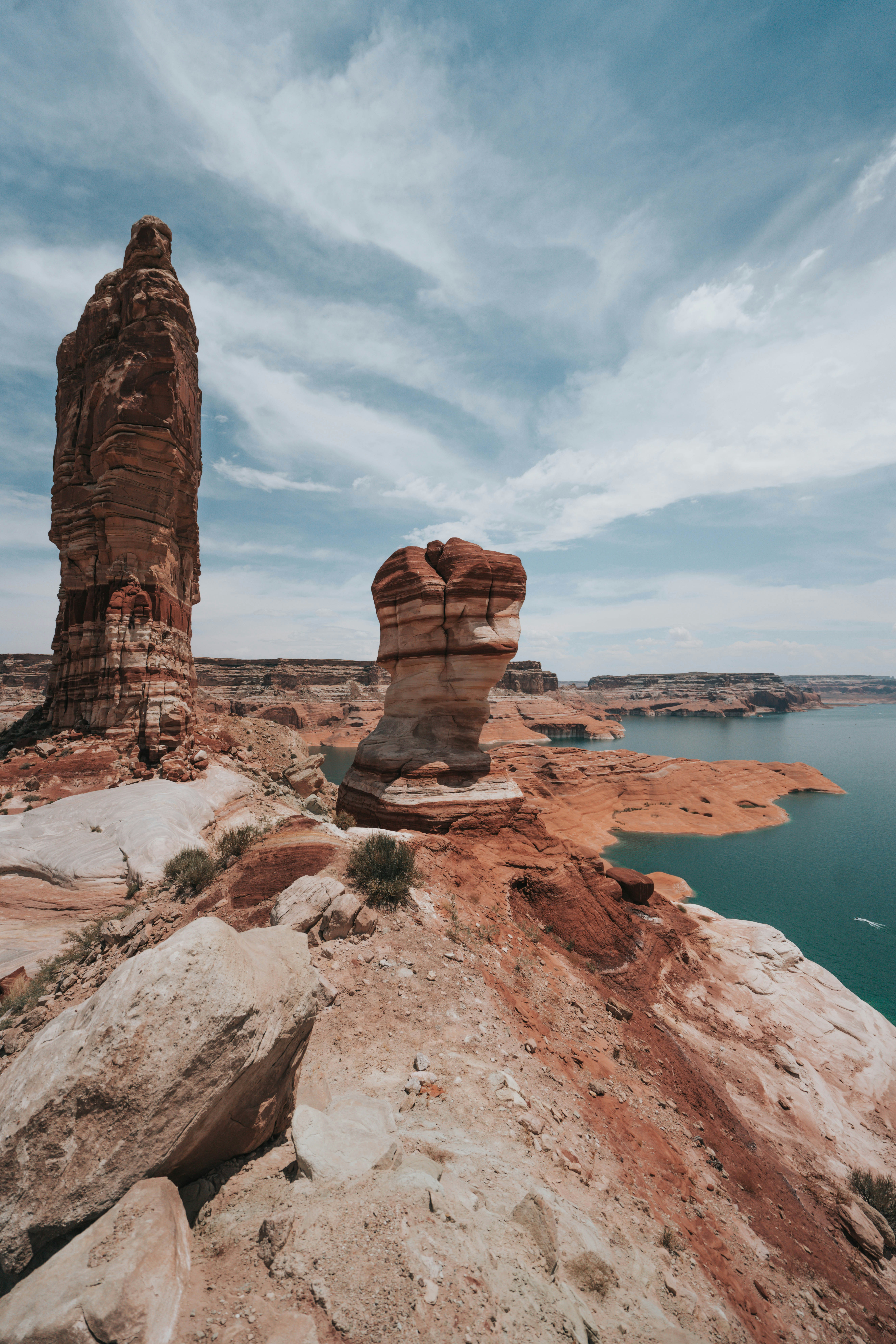 Two towering rock formations stand majestically above the tranquil waters of Lake Powell, showcasing the intricate patterns of erosion. The vibrant earth tones contrast beautifully with the blue lake below.