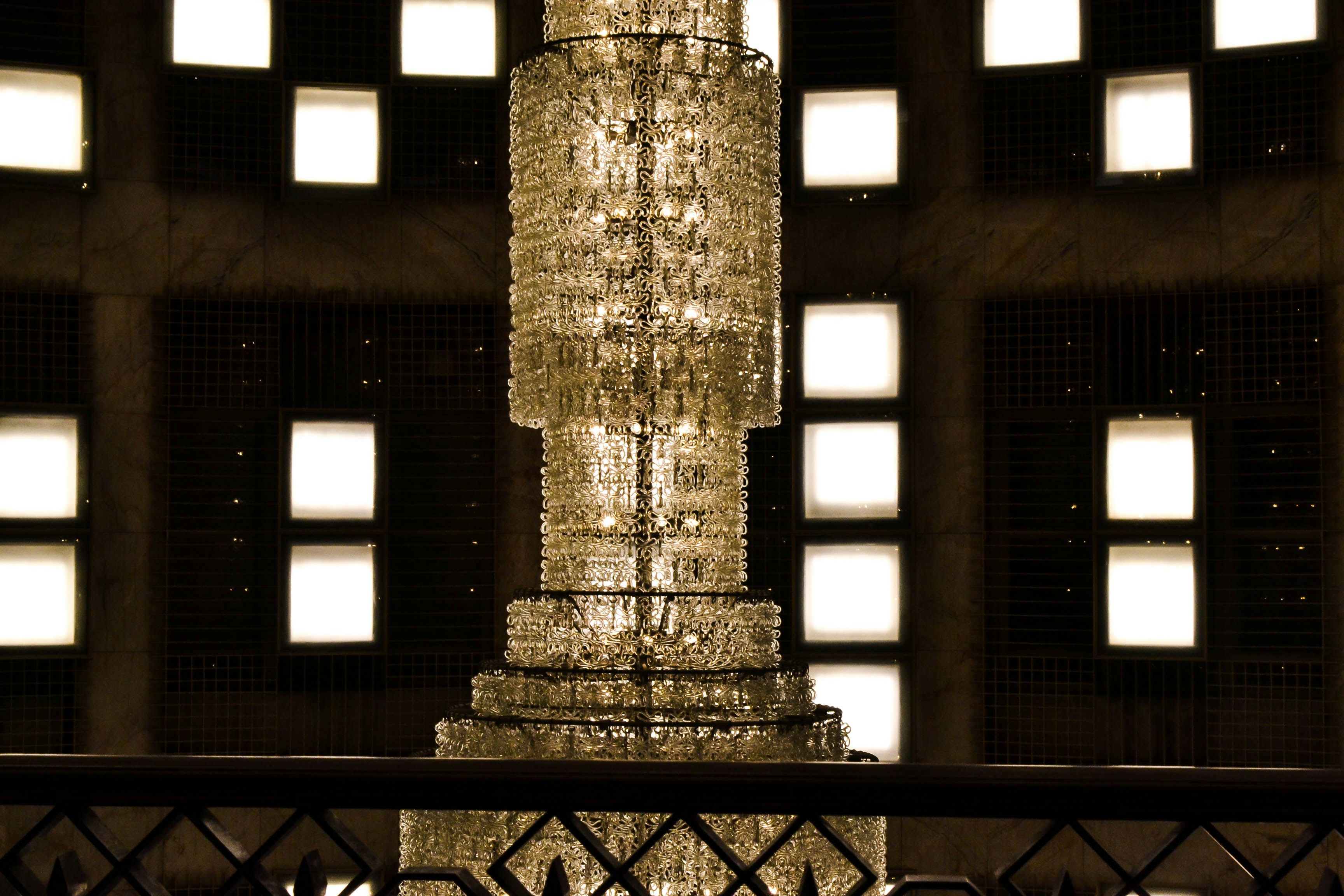 Ornate chandelier with cascading crystals against a backdrop of illuminated square windows.