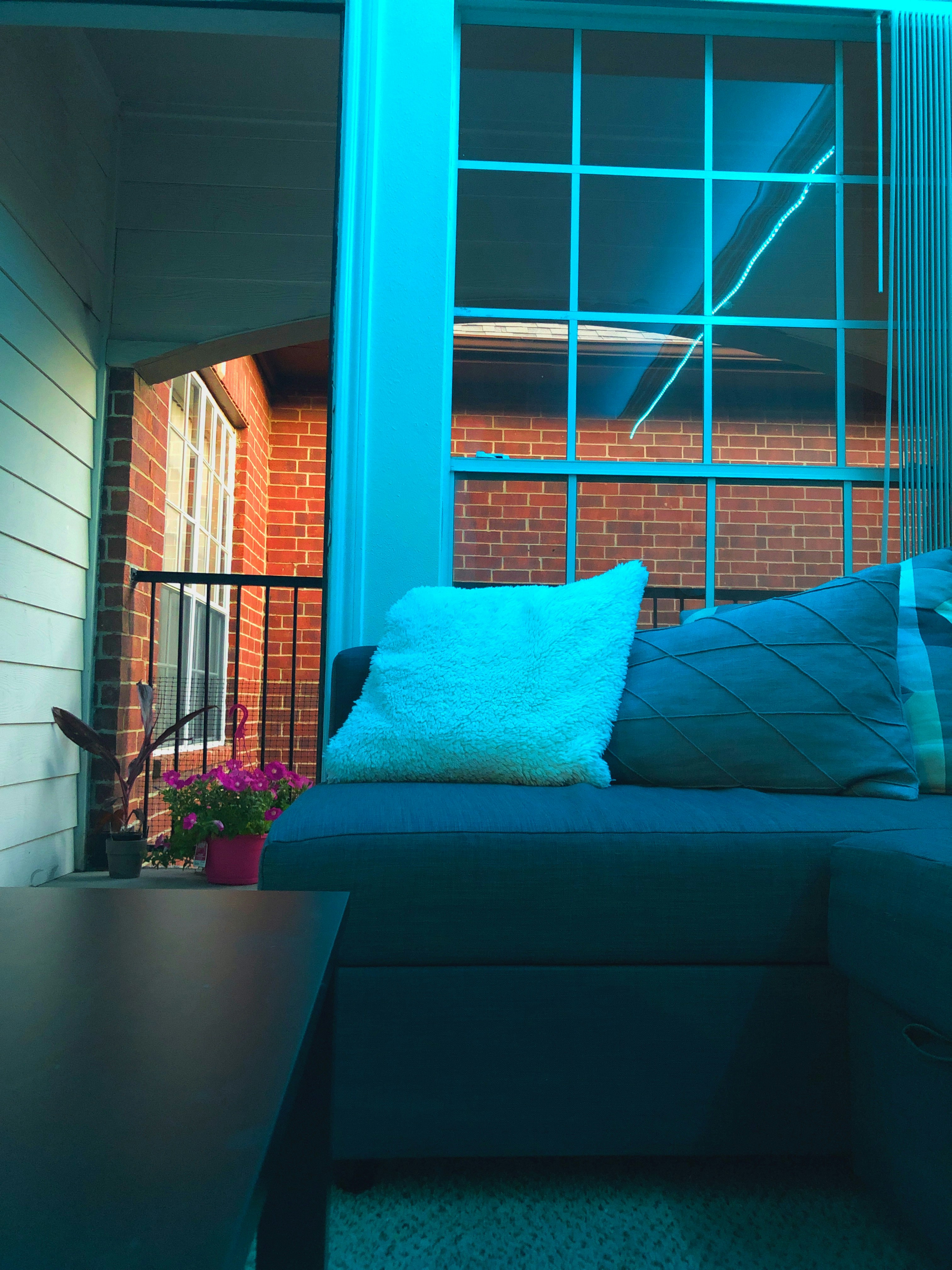 Blue-Glow Corner: Teal Couch and Brick Backdrop in a Quiet Porch