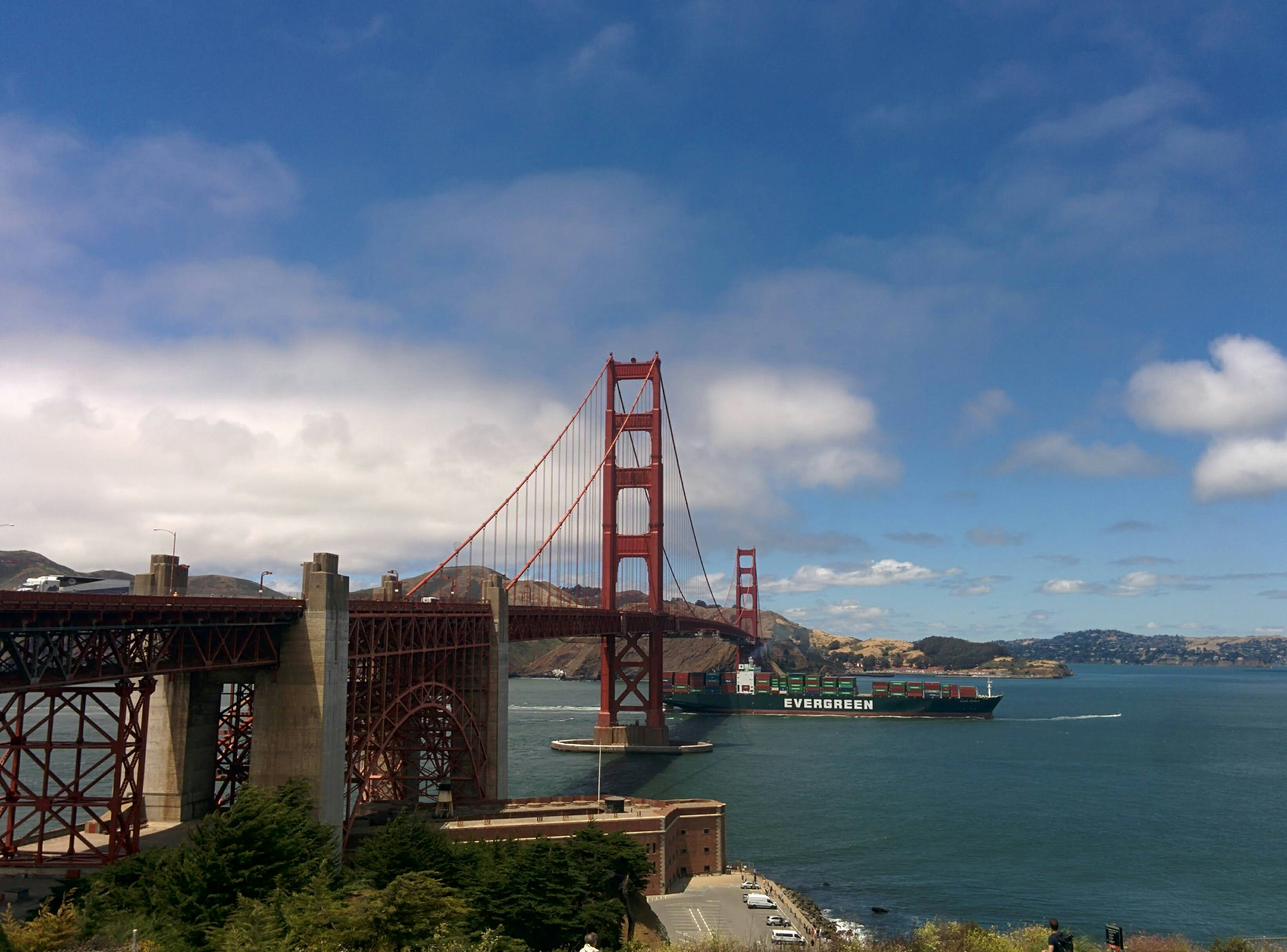 Golden Gate Bridge towering over a passing cargo ship, framed by a vibrant sky and coastal landscape.