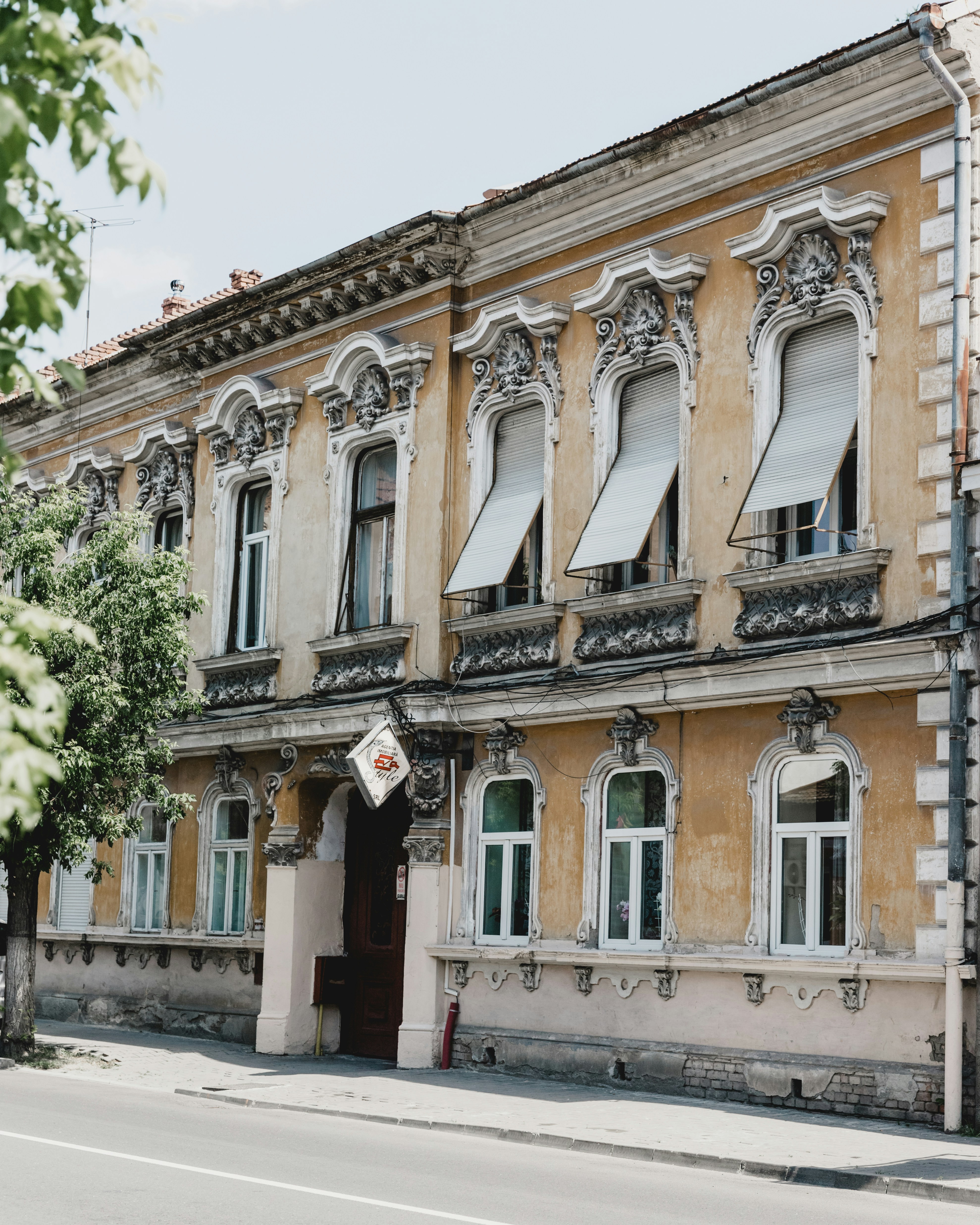 Ornate historical building with faded yellow exterior and partially closed shutters on a sunny day.