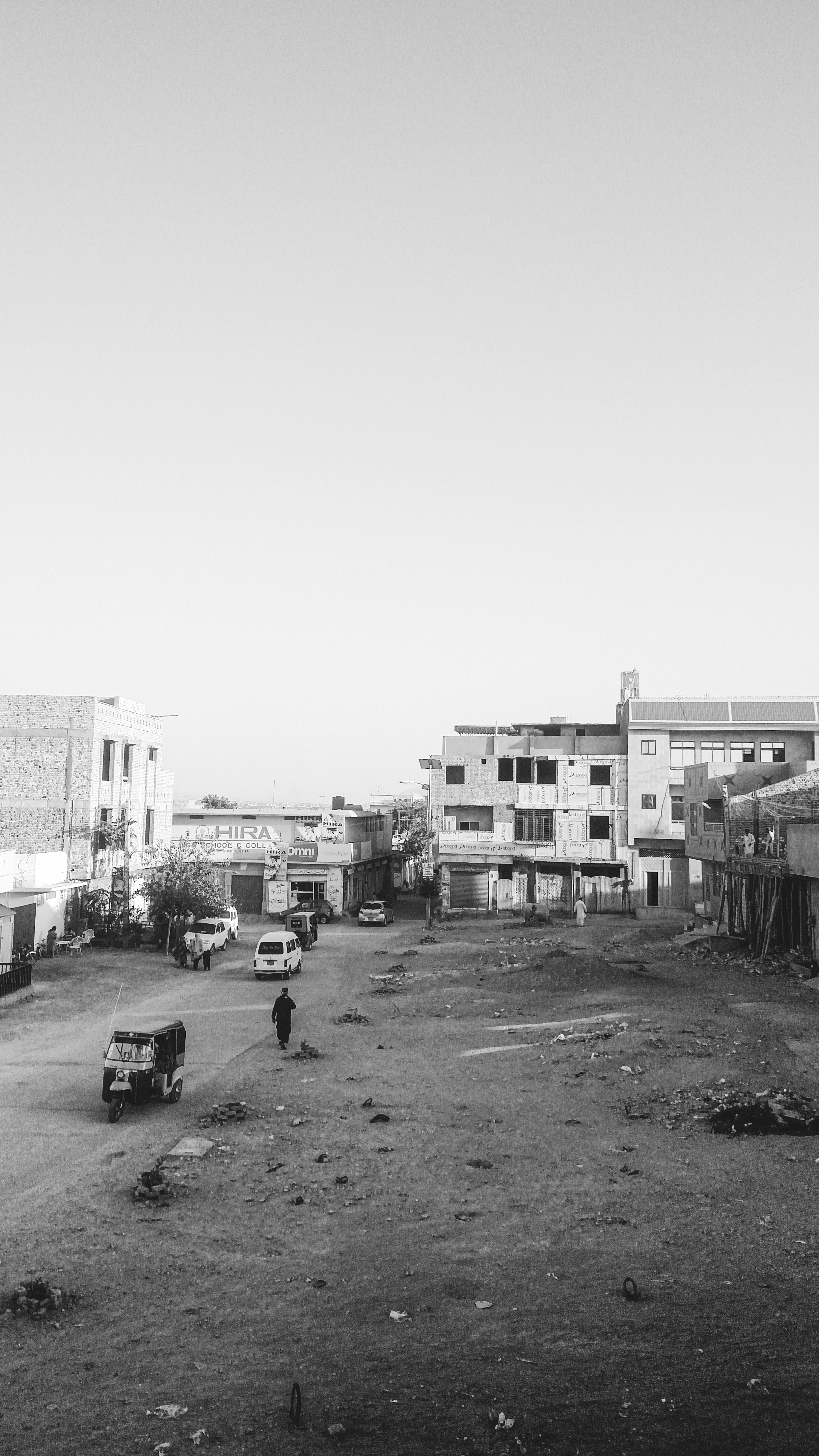 A quiet street scene in a bustling town, featuring a mix of vehicles and pedestrians amidst simple architecture. The monochrome palette emphasizes the tranquility of urban life.