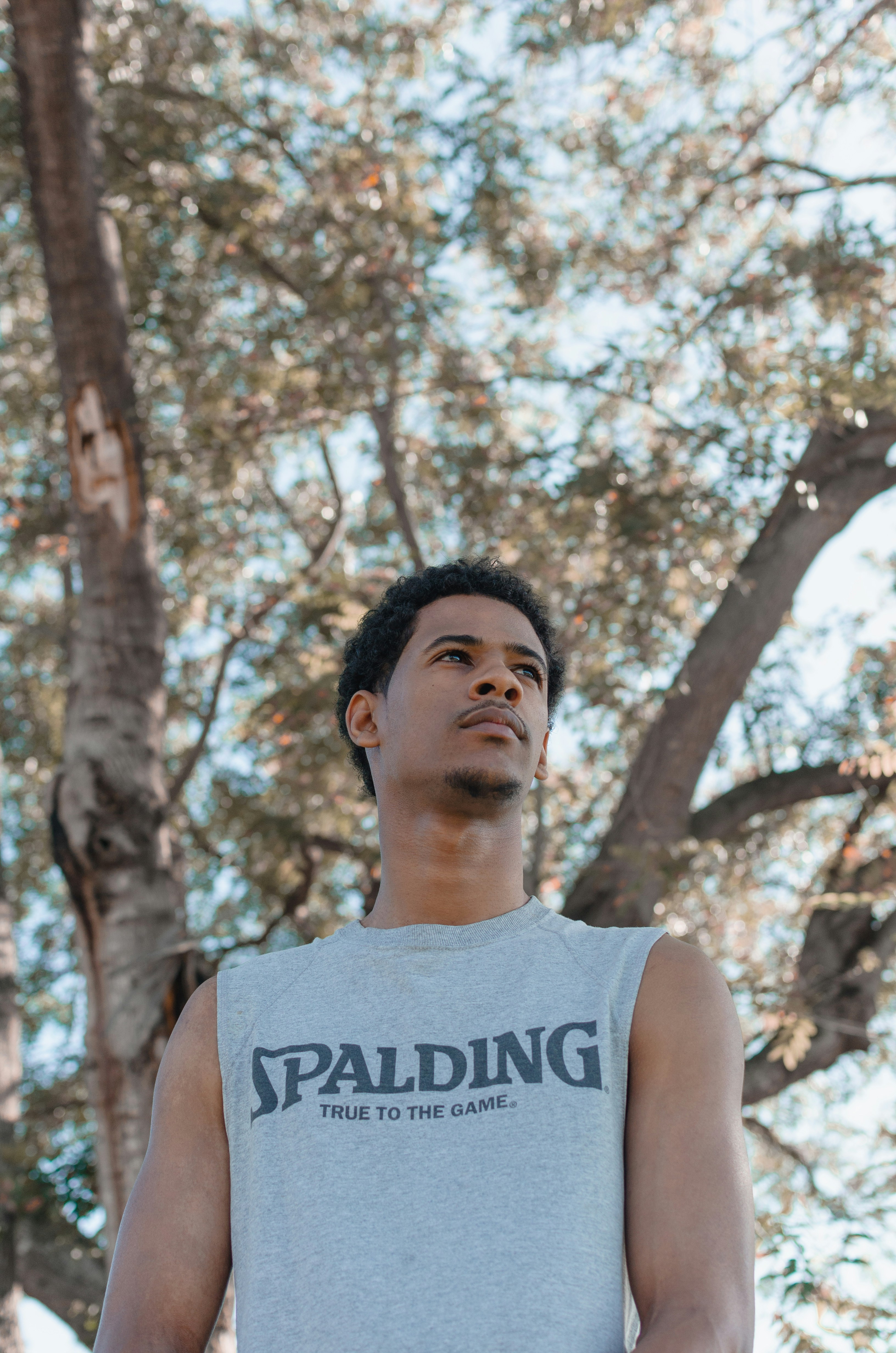 Man wearing gray Spalding tank top standing near tall trees photo ...