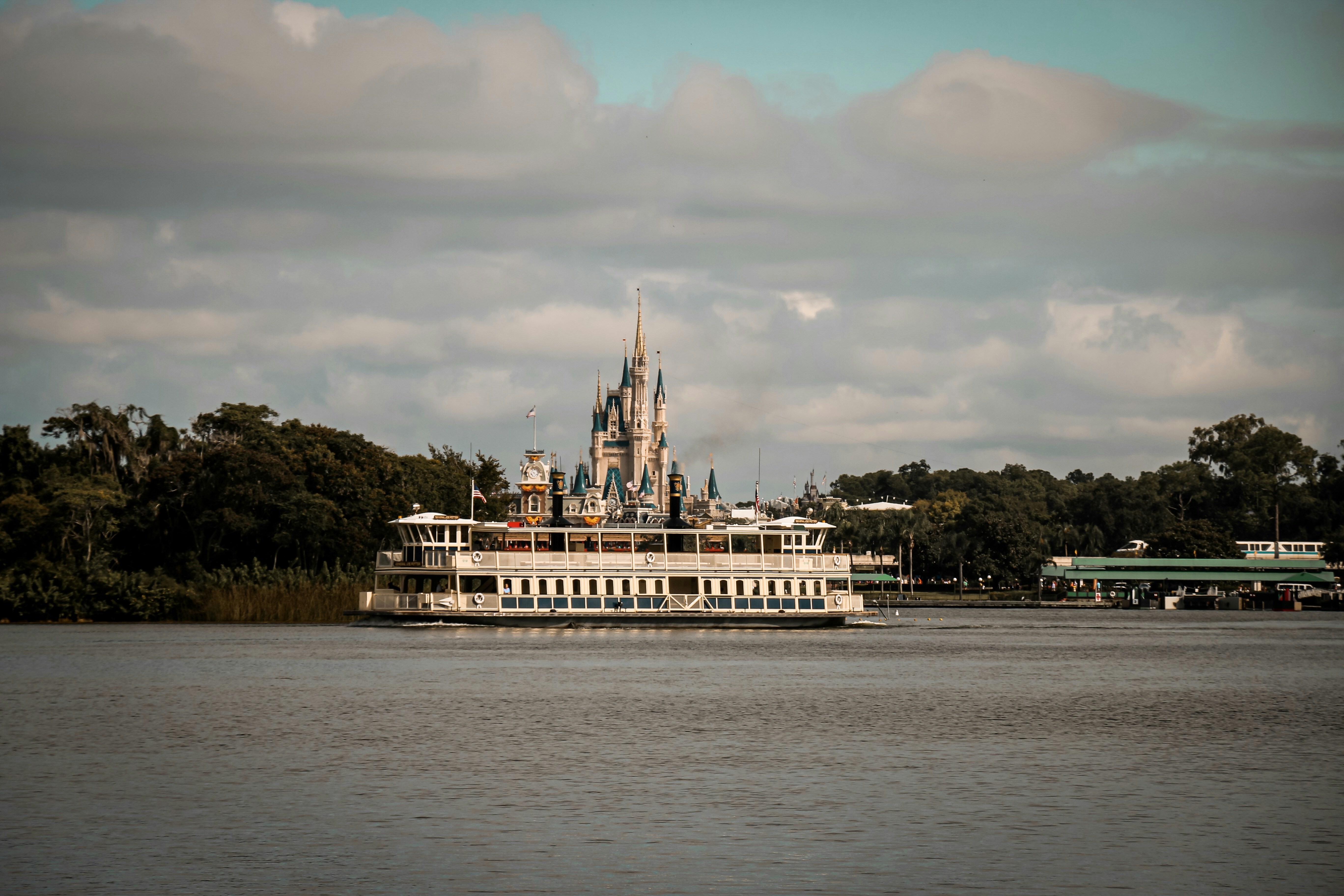 A vintage ferry glides across serene waters with a majestic castle in the background, surrounded by lush greenery. The scene evokes a sense of magical adventure.