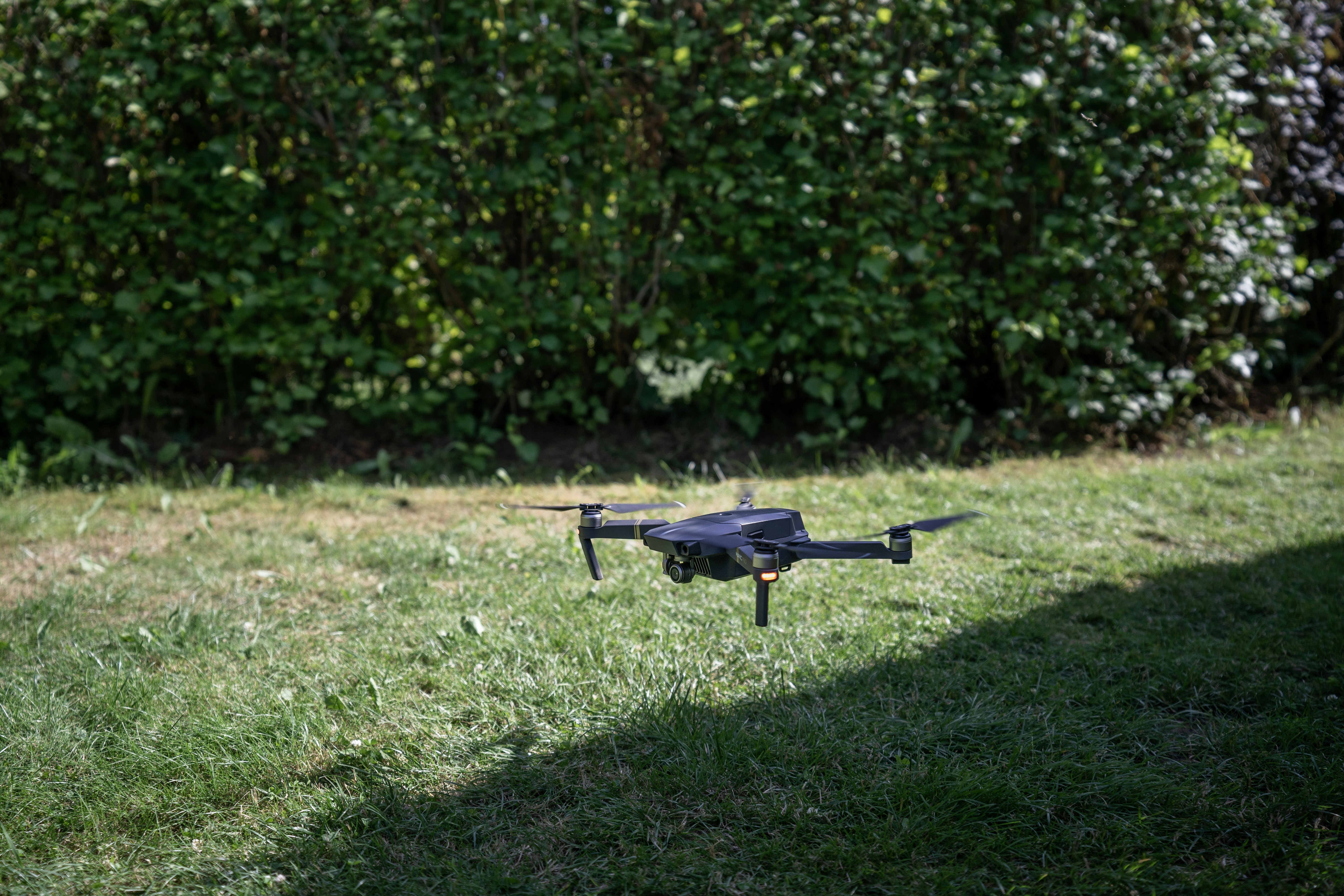 A drone hovers gracefully over a grassy area, surrounded by lush greenery. The scene captures the essence of aerial exploration.