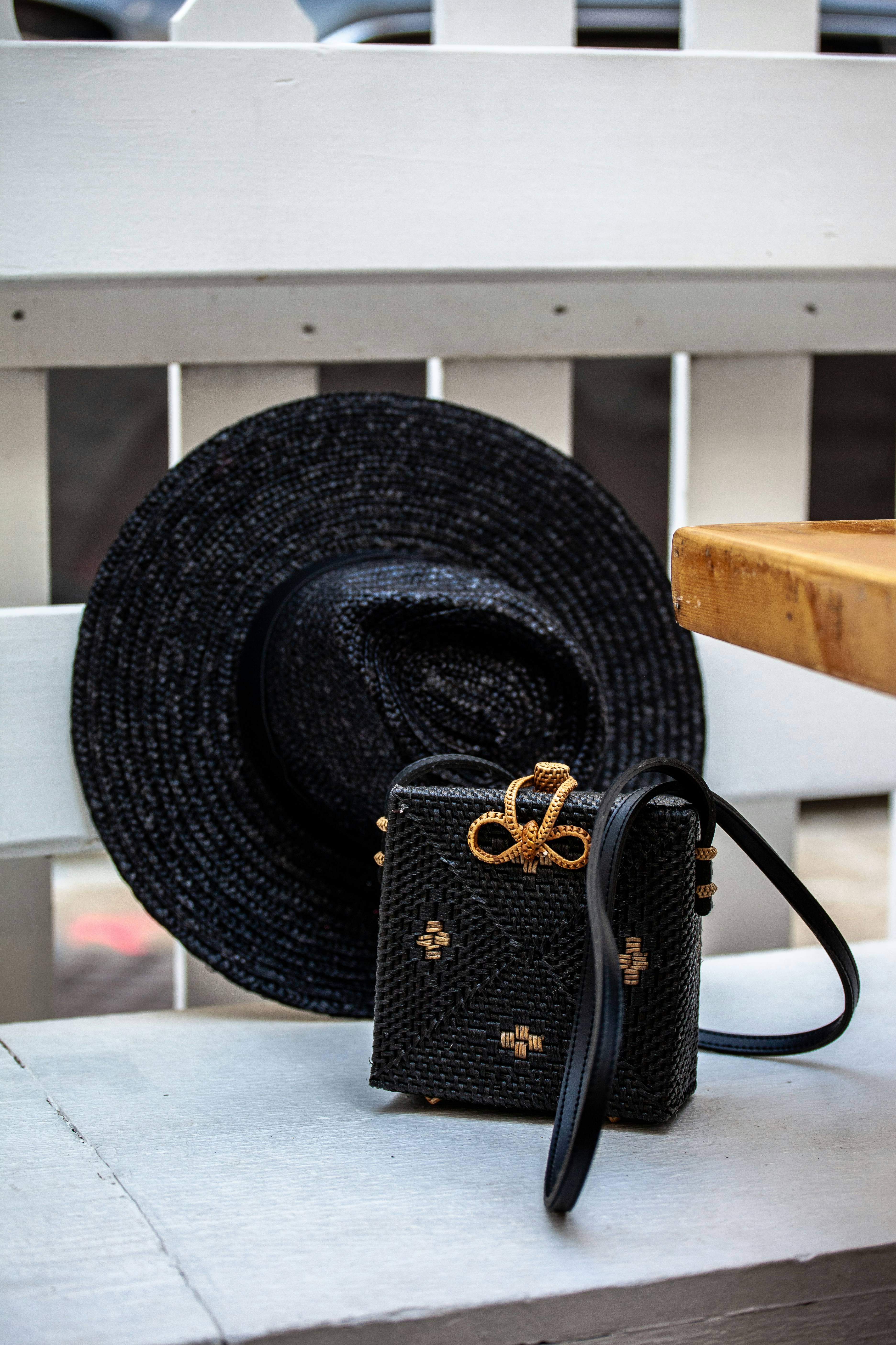Tiny Luxe on a White Bench: A Black Woven Handbag and Wide Hat
