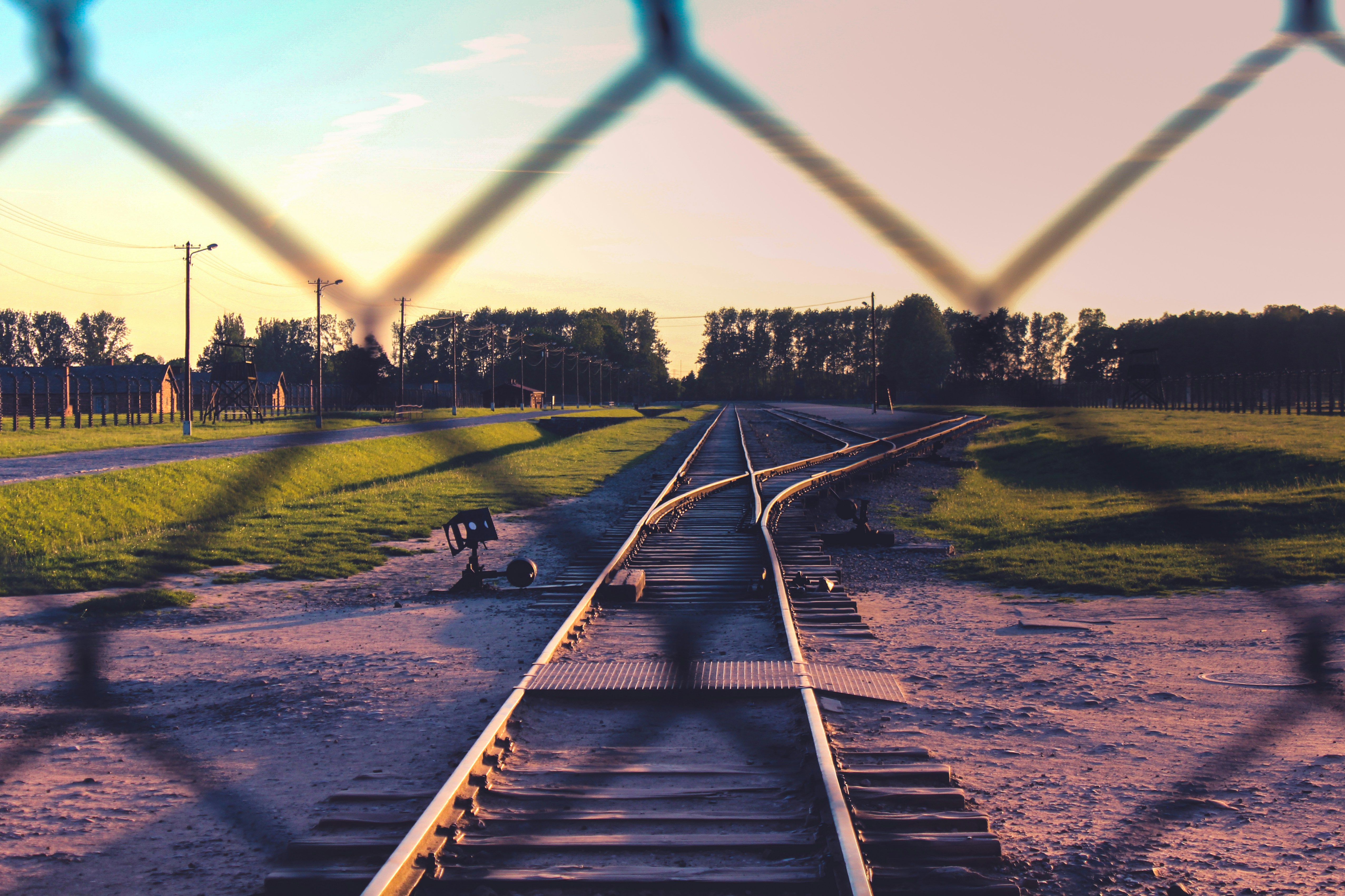 Railway tracks extend into the distance behind a chain-link fence under a warm sunset sky.