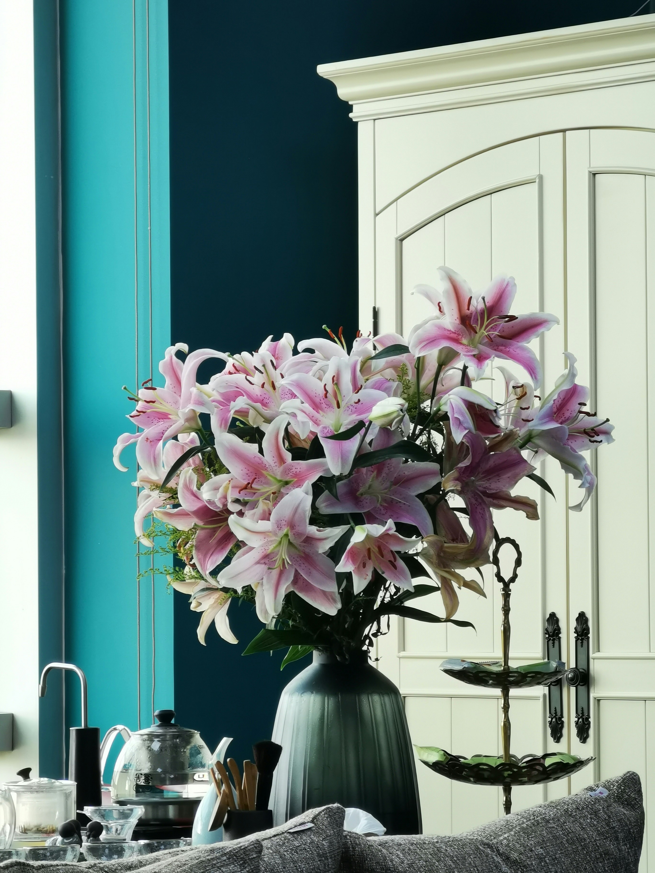 A vibrant bouquet of pink lilies in a sleek vase, set against a contrasting teal wall and elegant cabinetry. The composition highlights the harmony of natural beauty and modern decor.