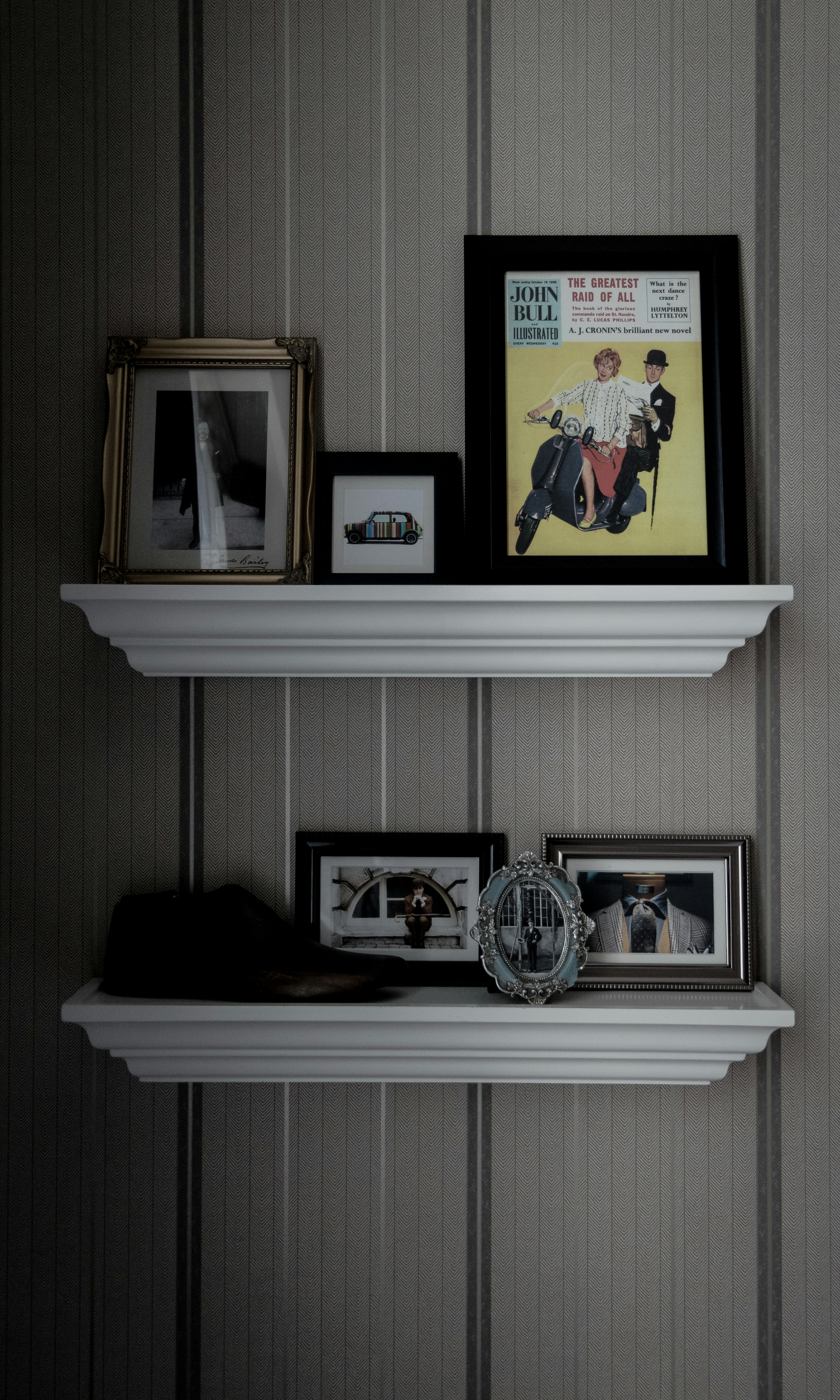 A collection of framed photographs and an illustrated magazine cover displayed on white shelves against a textured wall. The arrangement evokes a sense of nostalgia and personal history.