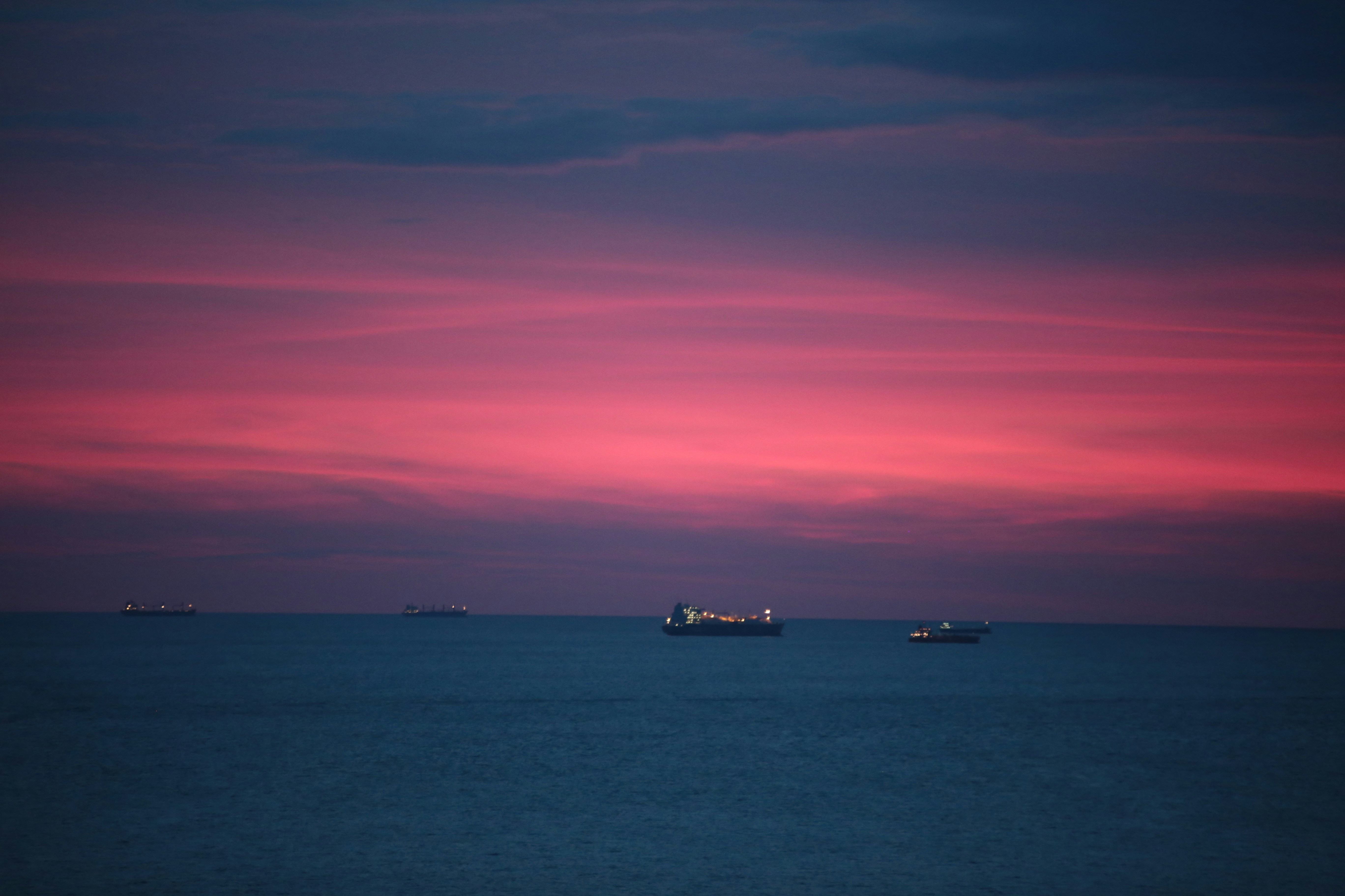 Cargo vessels waiting at the sea during sunset. | boats on body of water