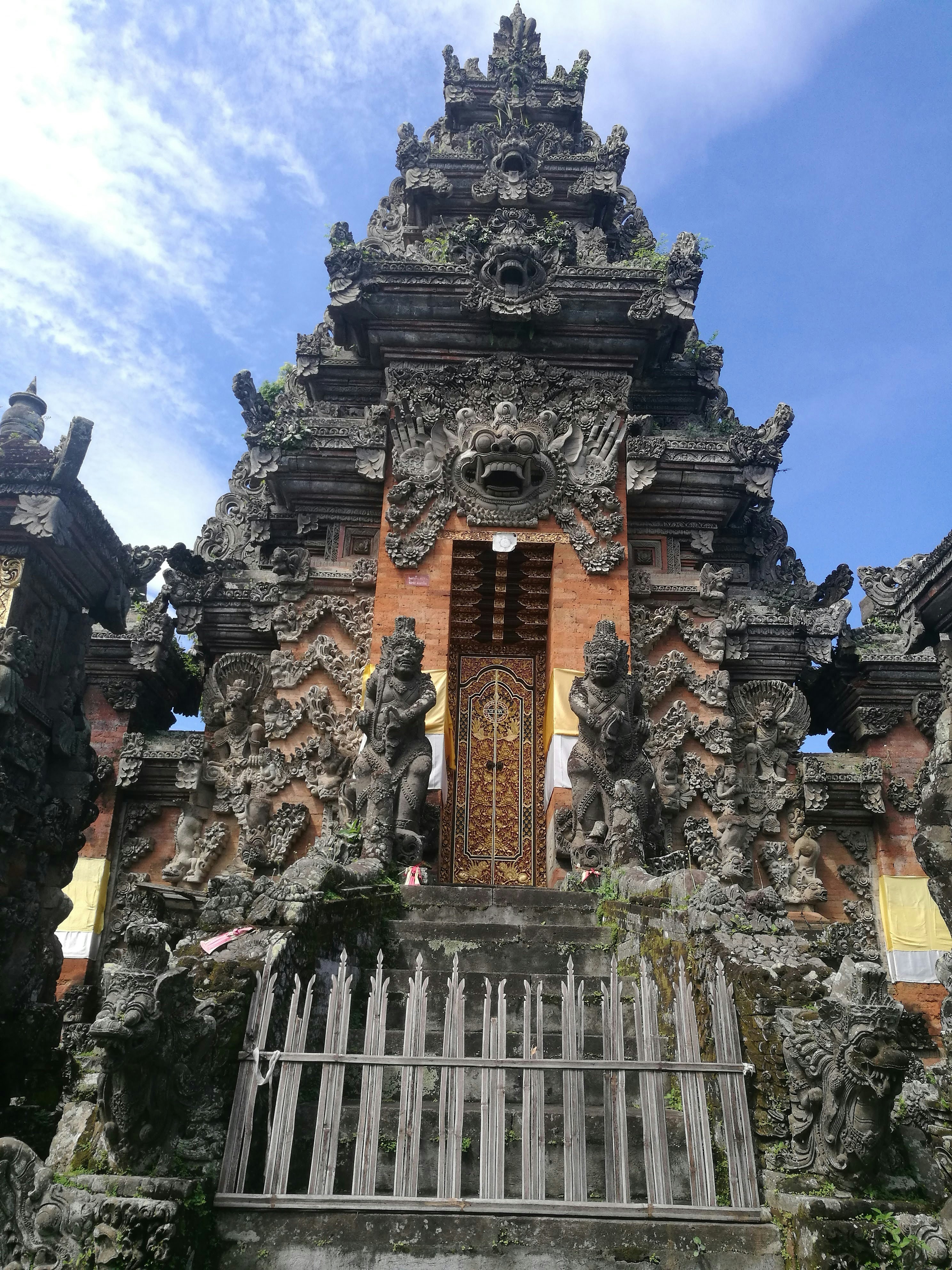 Intricately carved Balinese temple adorned with mythical figures and lush greenery, showcasing traditional architectural artistry.