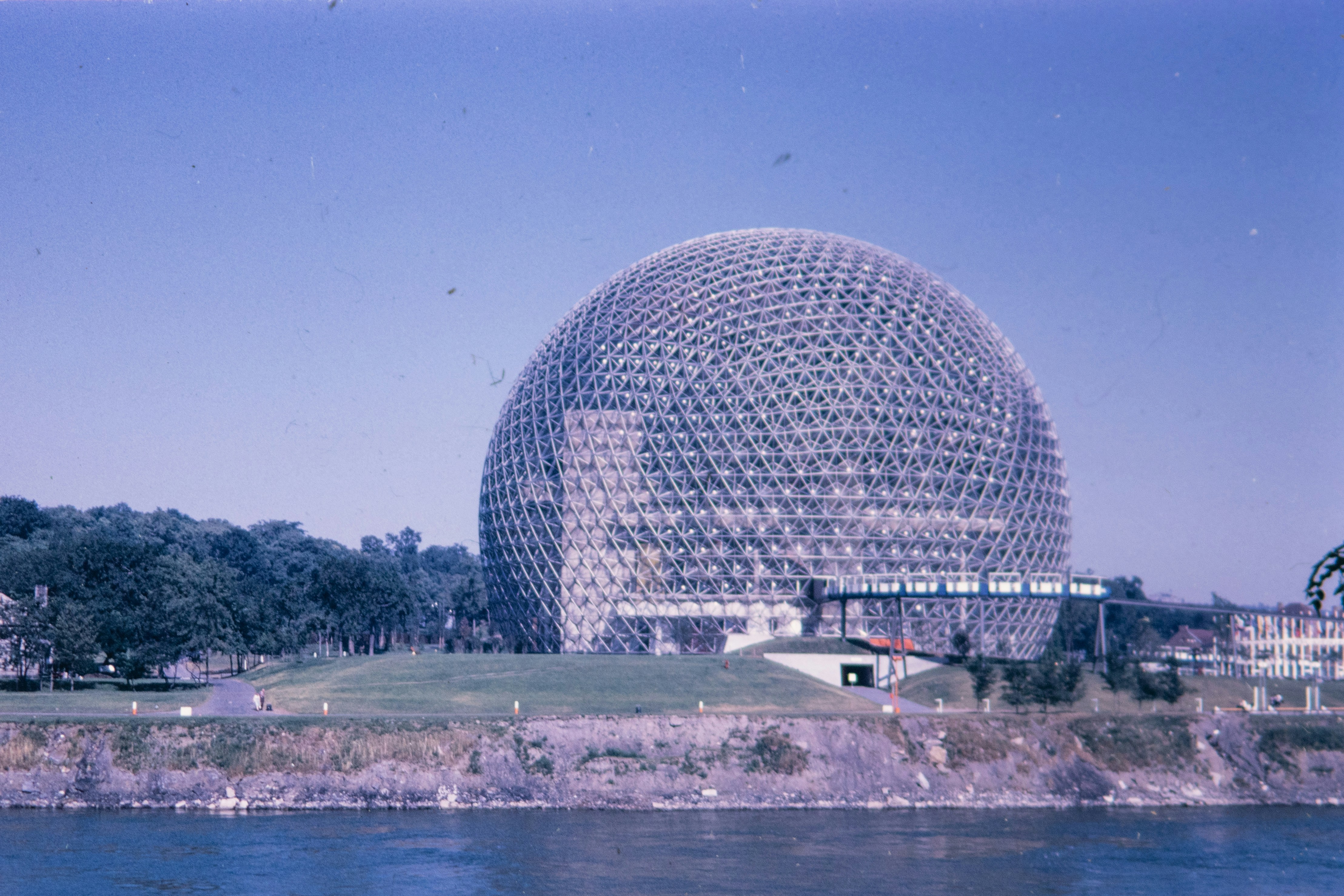Iconic geodesic dome structure surrounded by lush greenery and a calm river, showcasing innovative design and engineering.