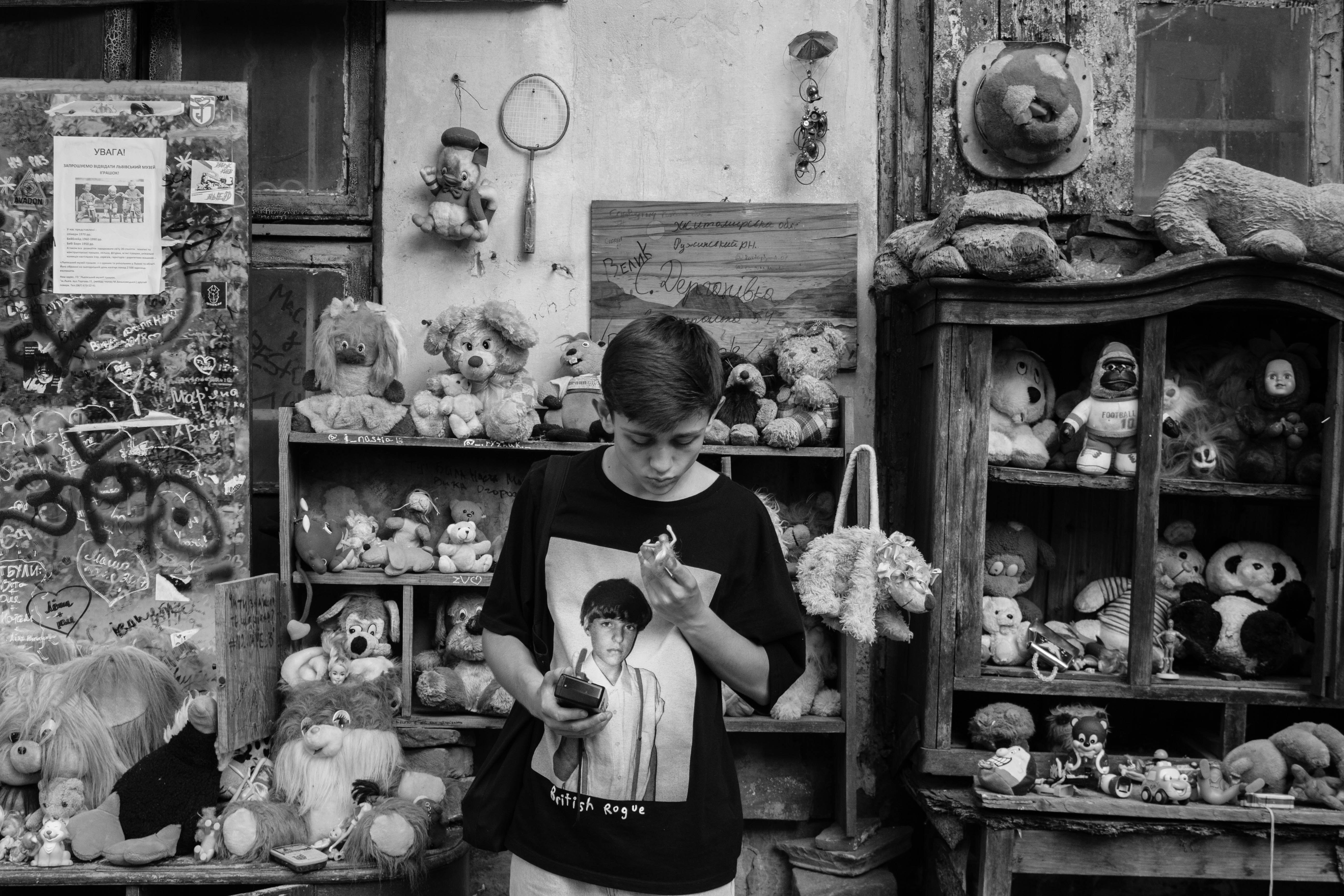 A boy engrossed in his phone stands amidst a vibrant collection of vintage toys and trinkets, evoking a sense of nostalgia. The scene is rich in textures and character.