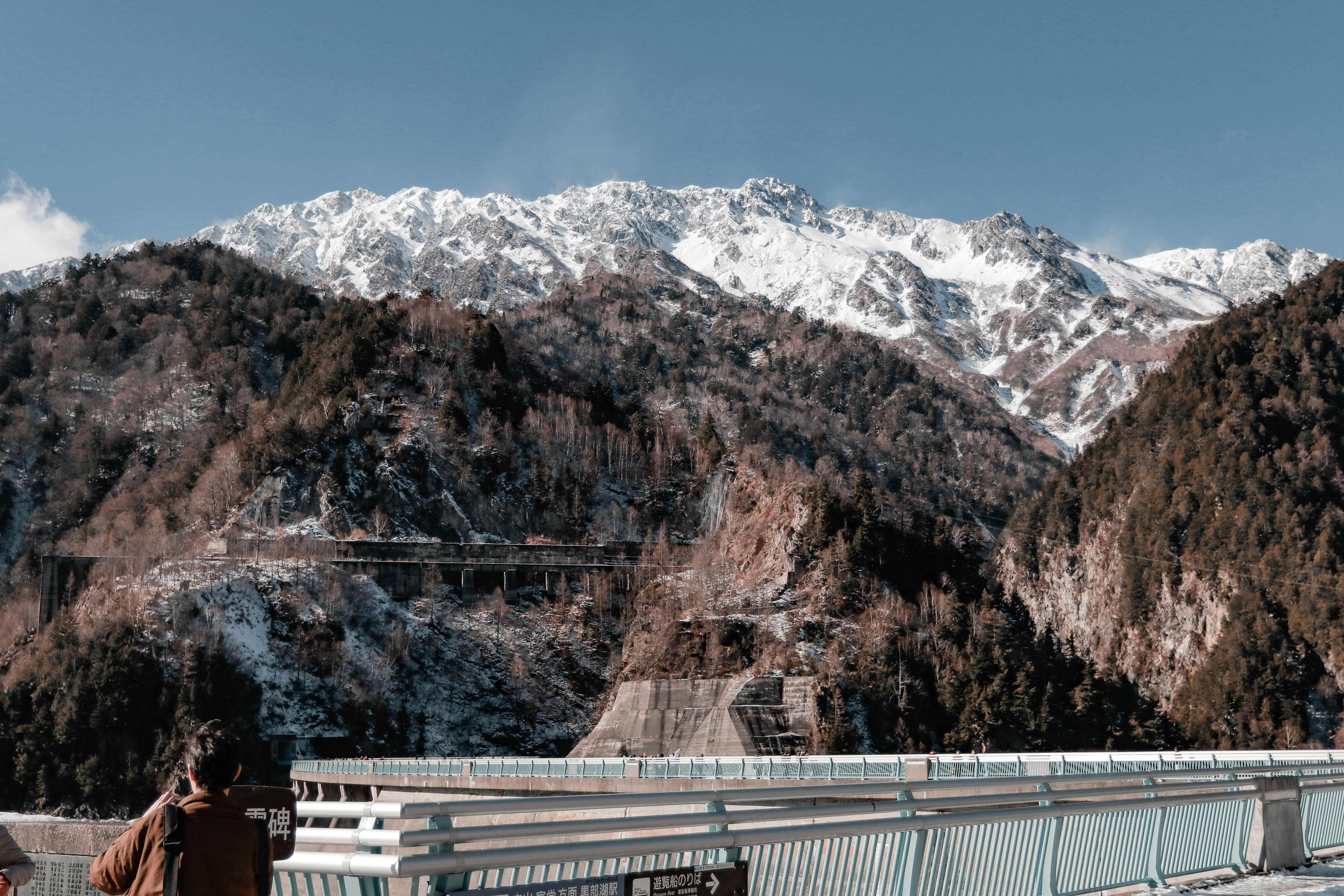 Snow-capped mountains loom over a scenic landscape, with a photographer capturing the serene beauty from a vantage point. The scene reflects the tranquility of nature in winter.