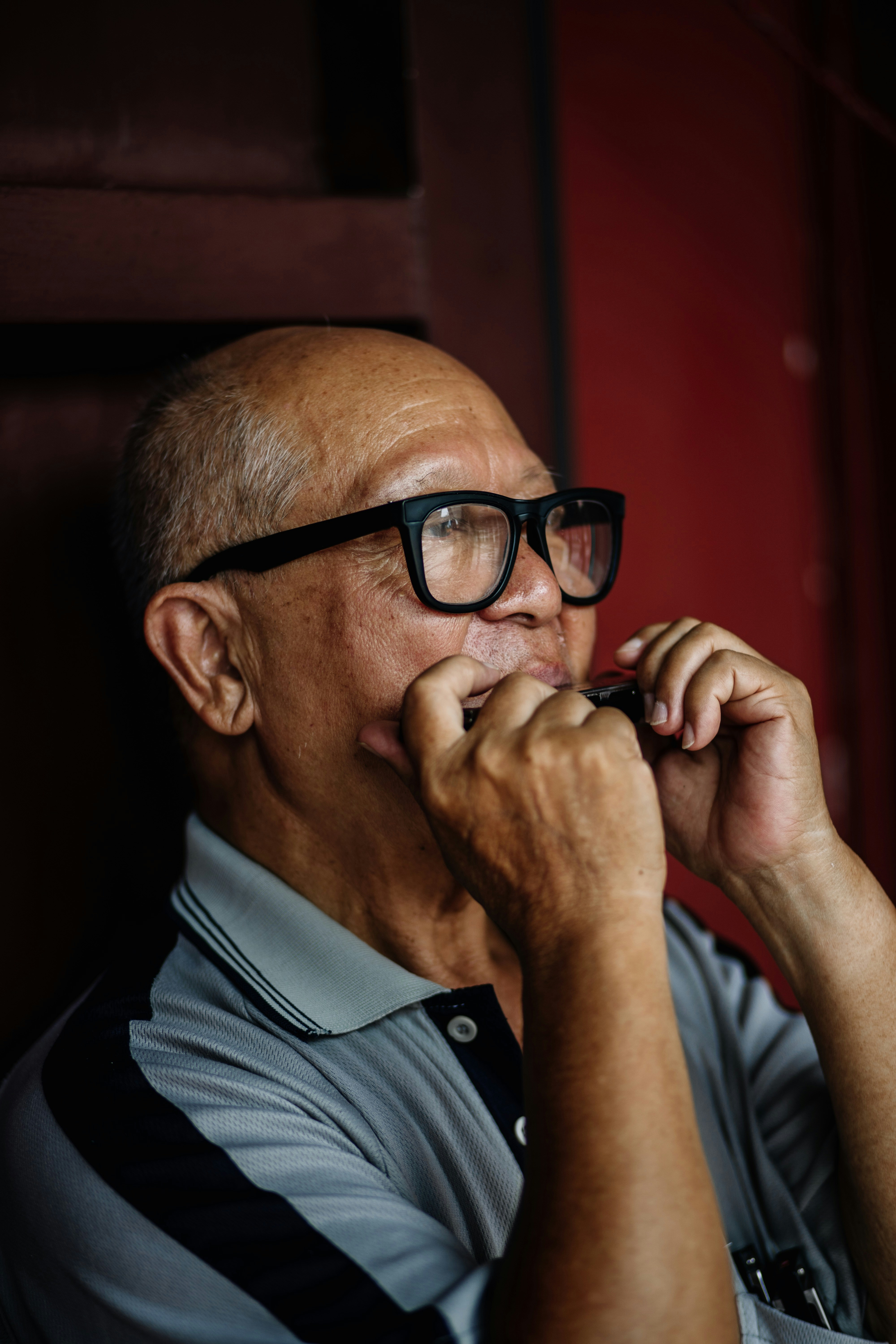 Elderly man playing a harmonica, immersed in music, with a warm backdrop highlighting his expressive features.