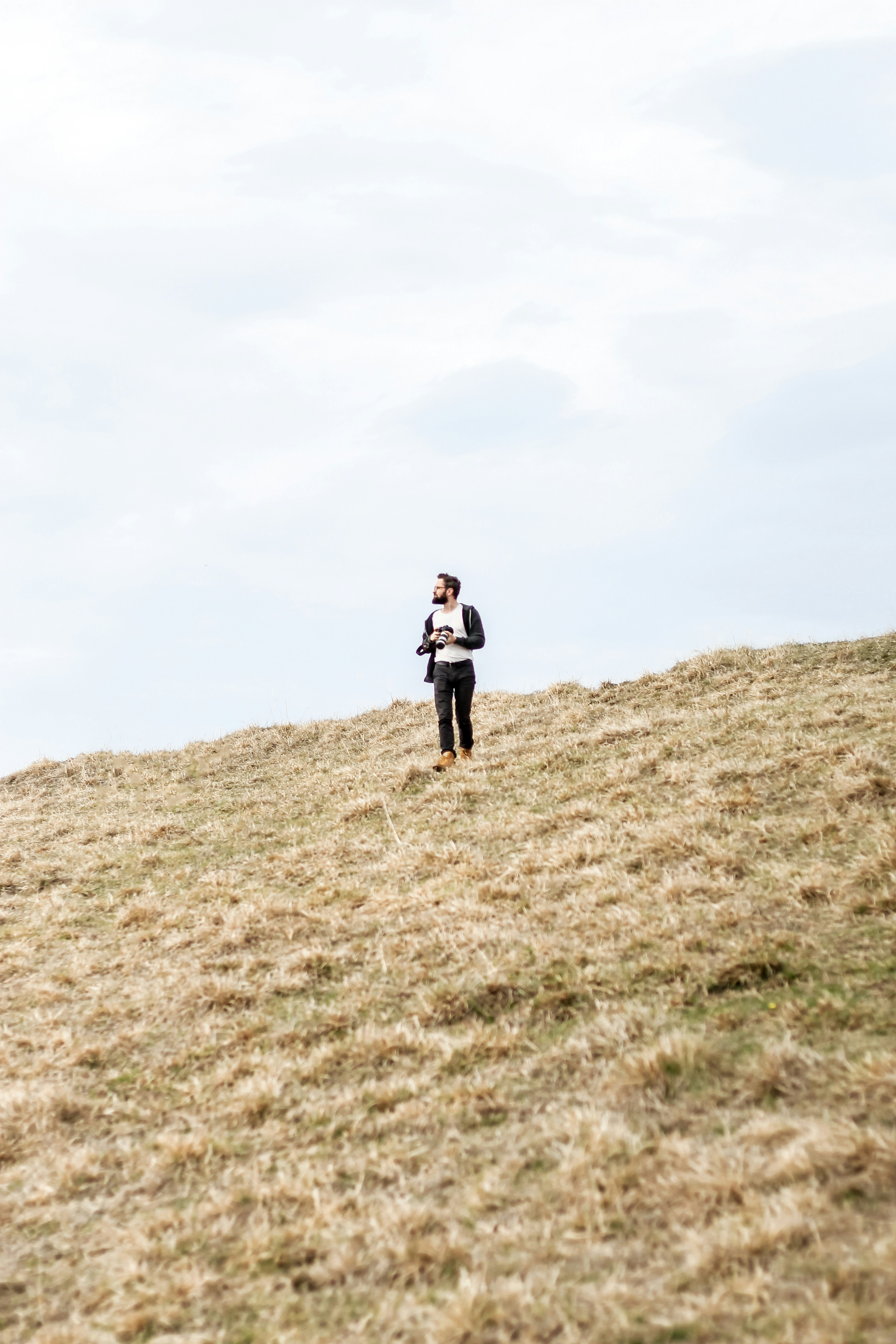 Person standing on a grassy hill under an expansive cloudy sky.