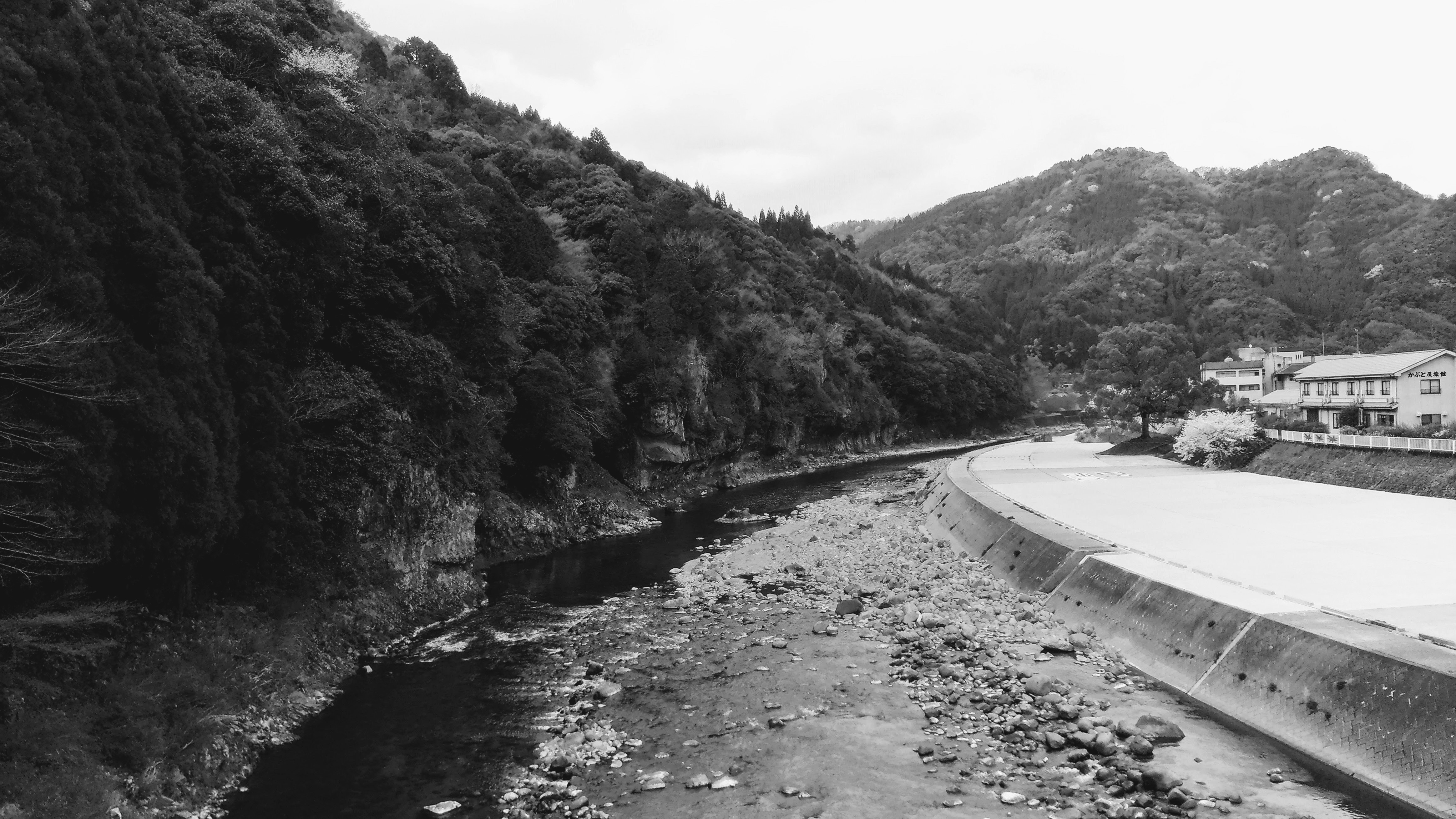 Black and white landscape of a winding river flanked by mountains and a small settlement.