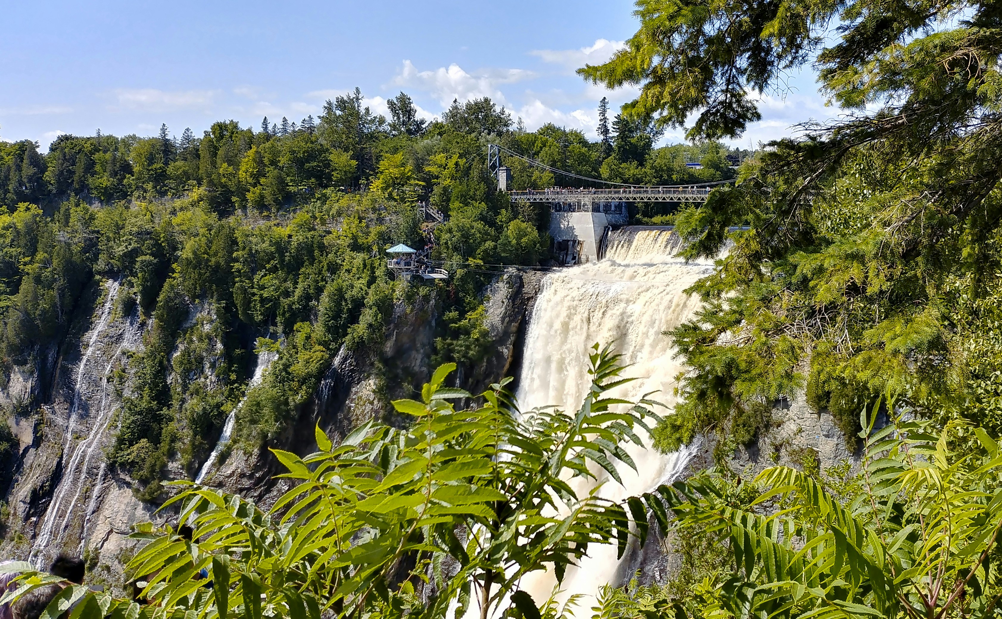 Waterfall plunging over a rocky cliff surrounded by dense green foliage under a clear blue sky.