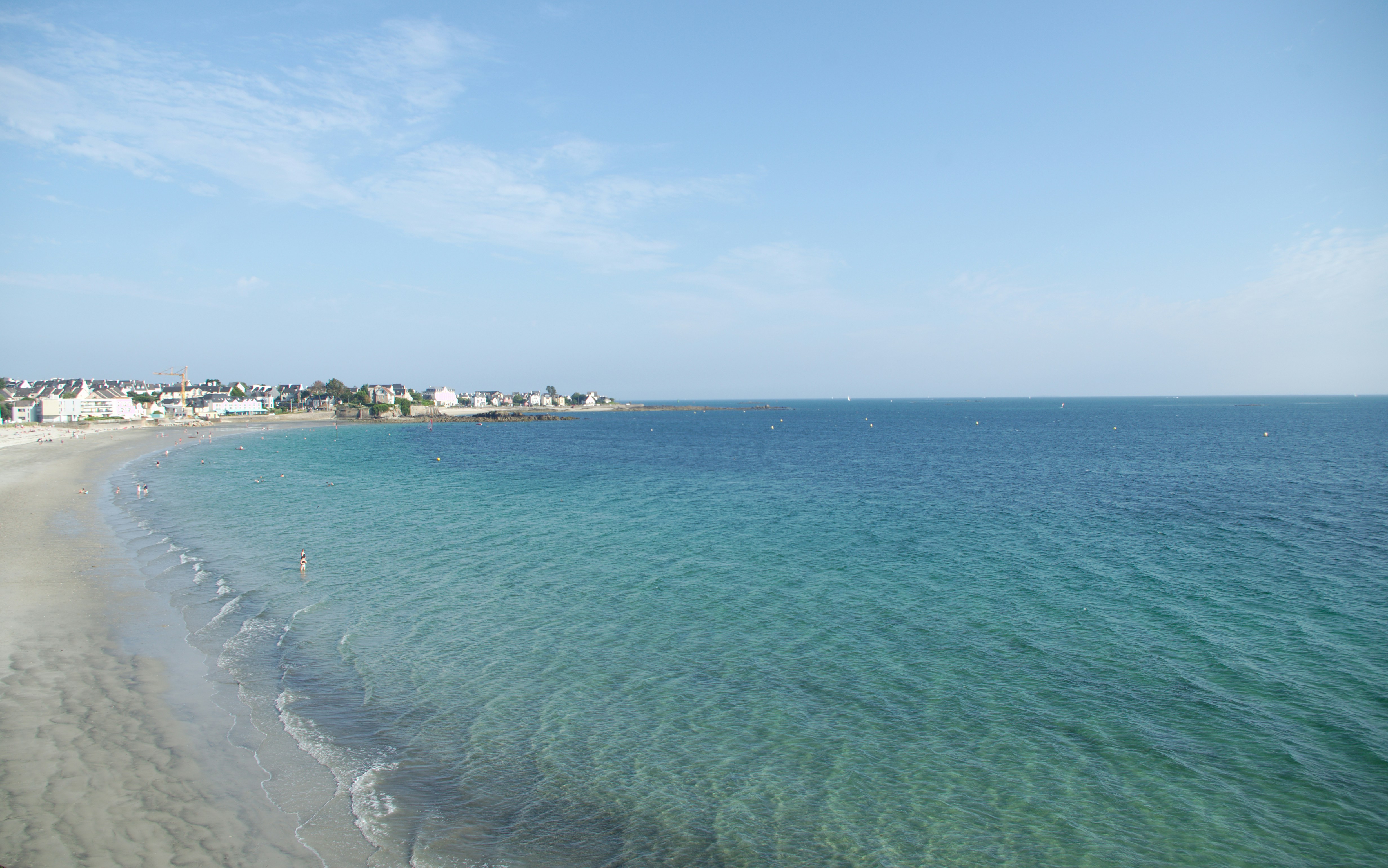 Clear blue waters meet a sandy beach under a bright sky.