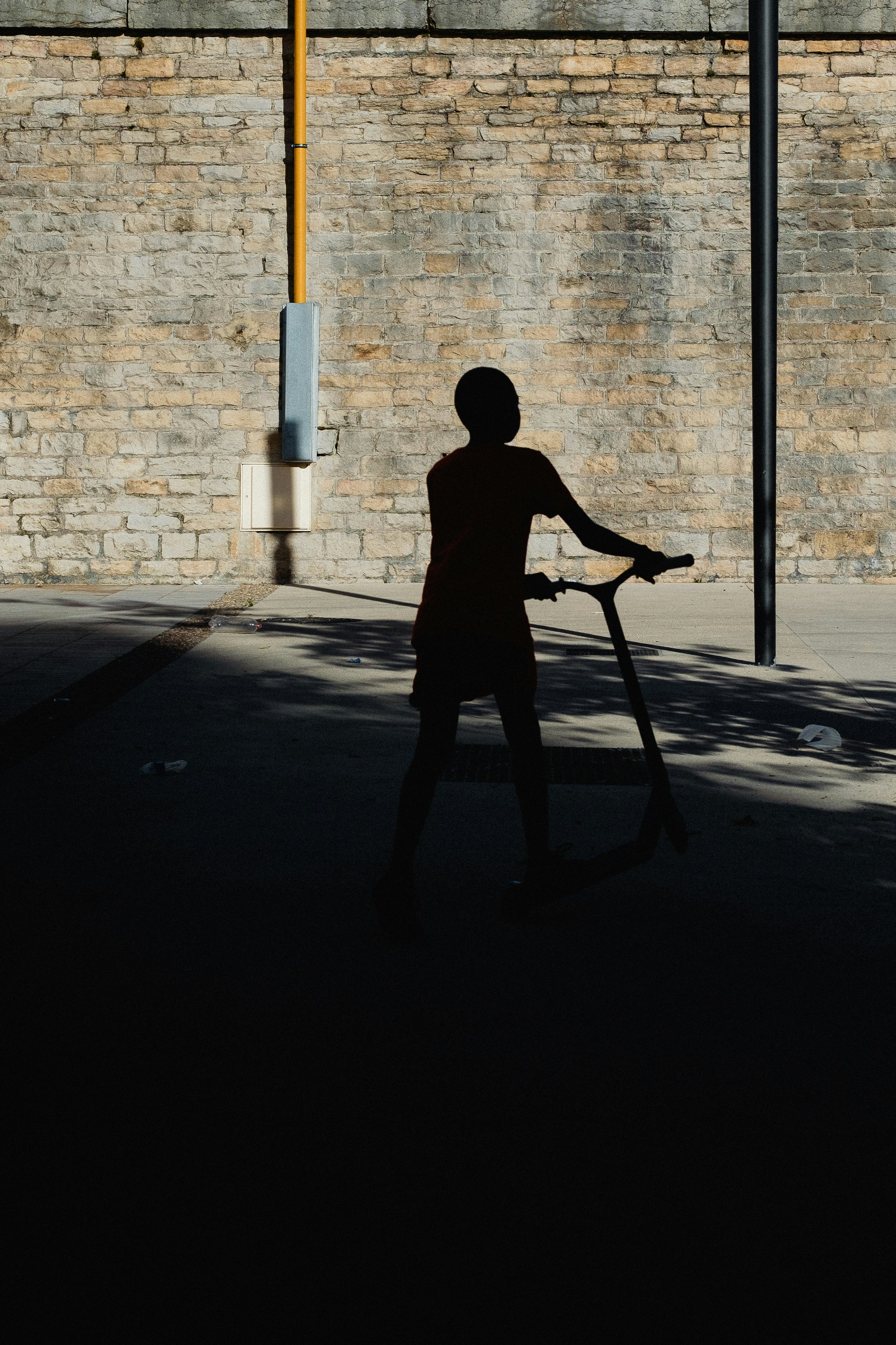 Edge of Light: Silhouette of a Rider with Scooter Against a Brick Wall