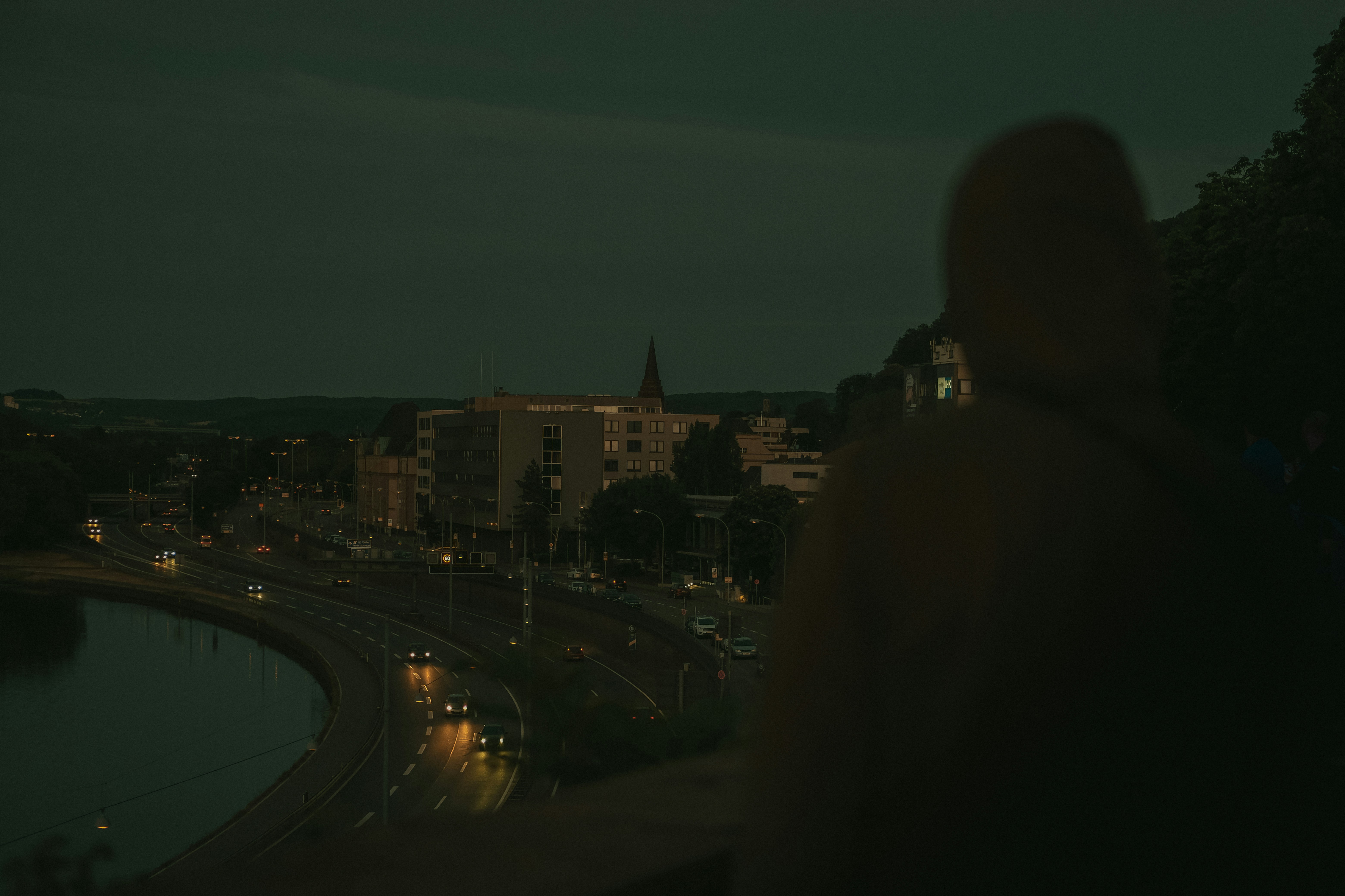 Riverside Nightscape: City Lights Trace the Bend from a Balcony Silhouette