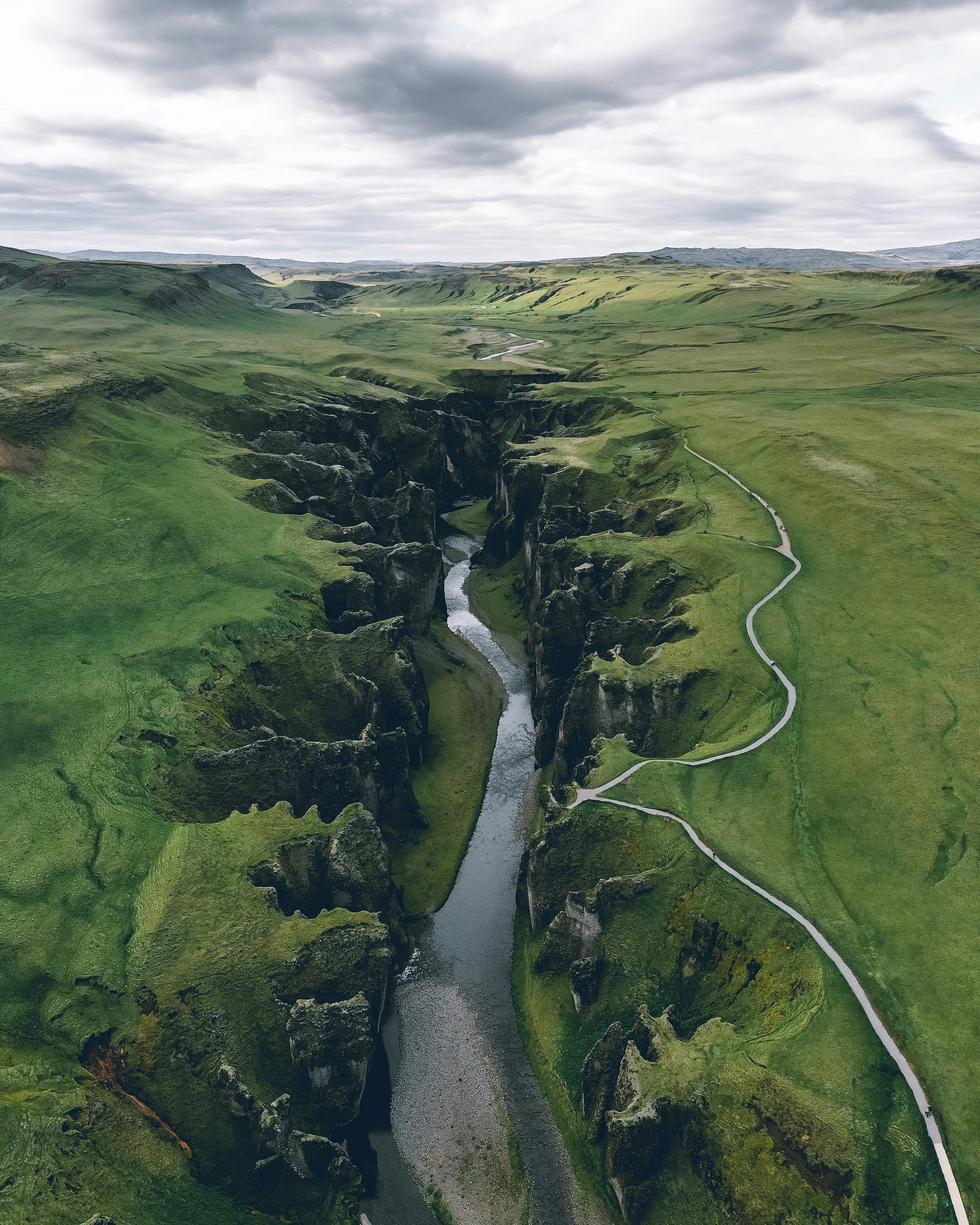 Aerial view of a winding river flowing through a dramatic canyon surrounded by lush greenery. The path meanders alongside the rugged cliffs, showcasing the natural beauty of the landscape.