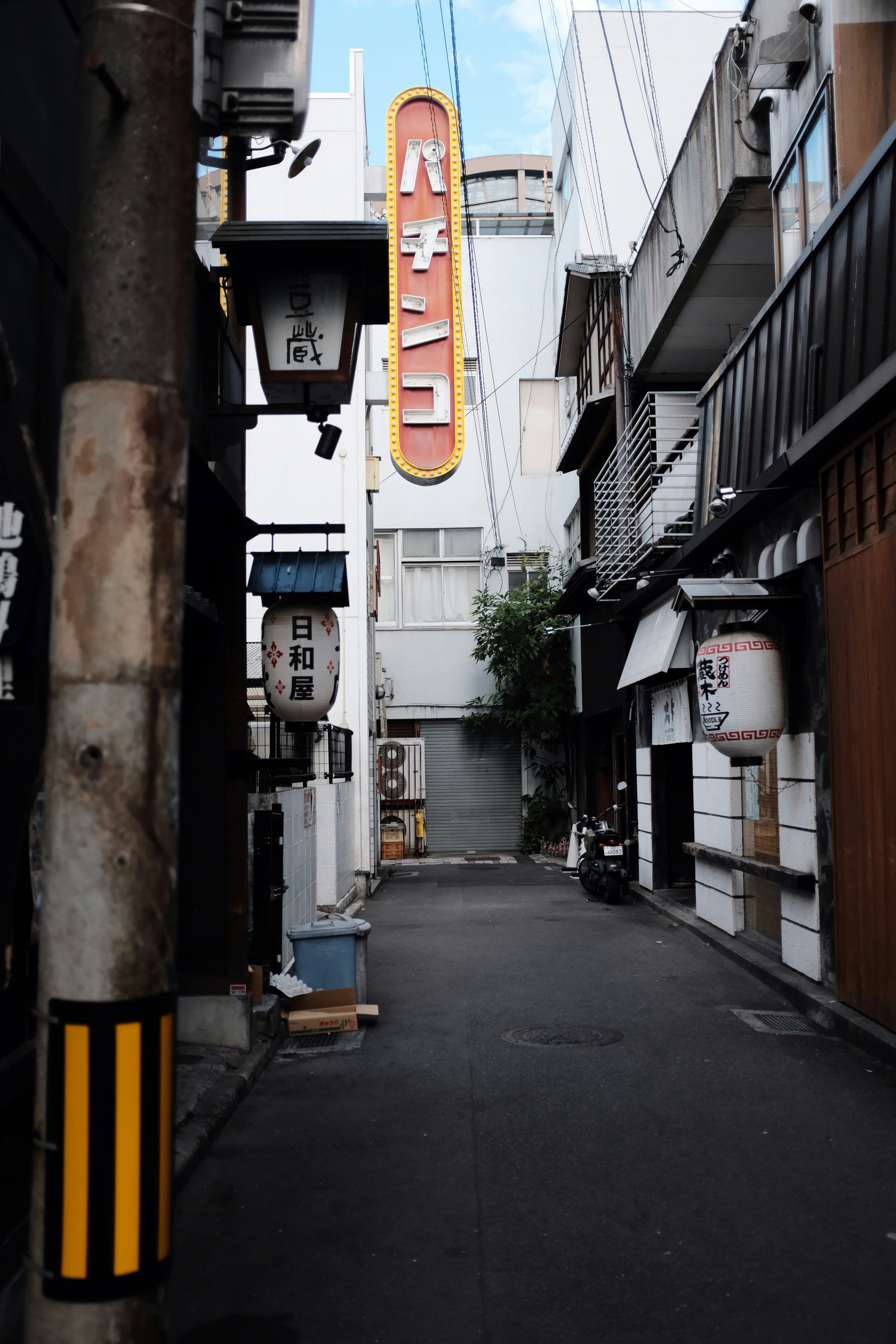 A narrow alleyway lined with traditional signage and a prominent neon sign above, suggesting a lively atmosphere in a bustling urban environment.